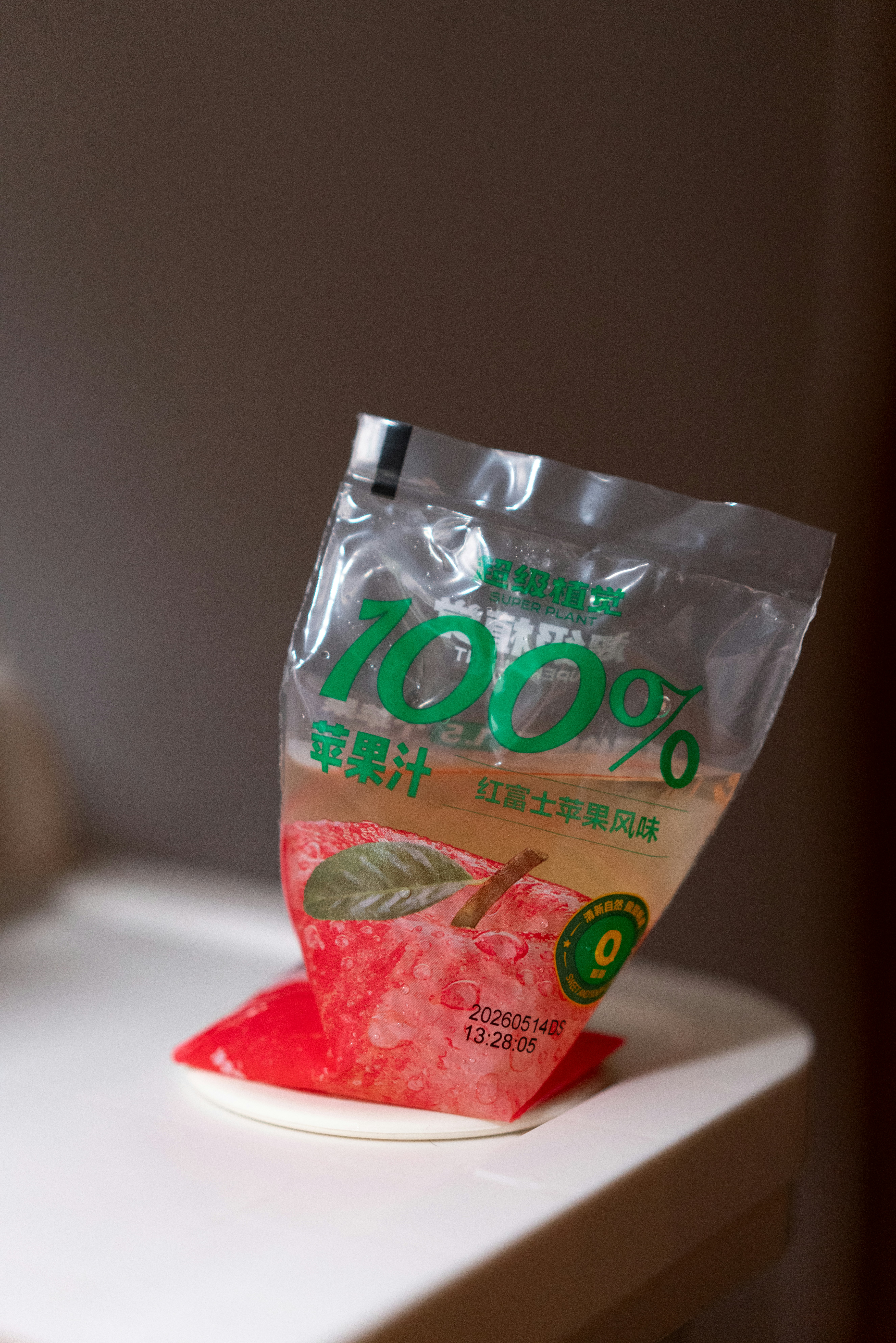 A sealed 100% apple juice pouch sits on a white surface with soft background blur.