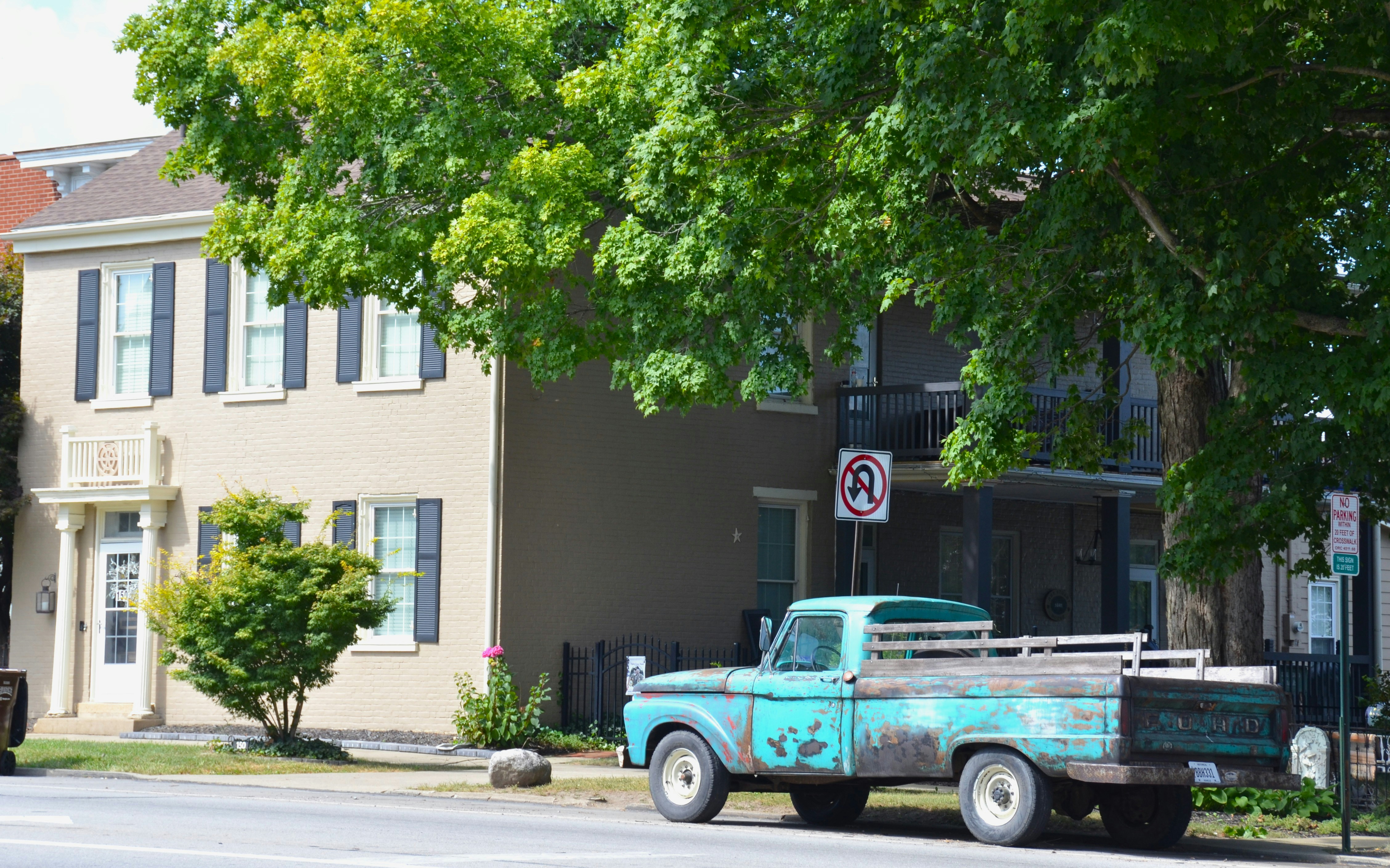 Weathered turquoise truck under leafy shade by a quiet suburban street