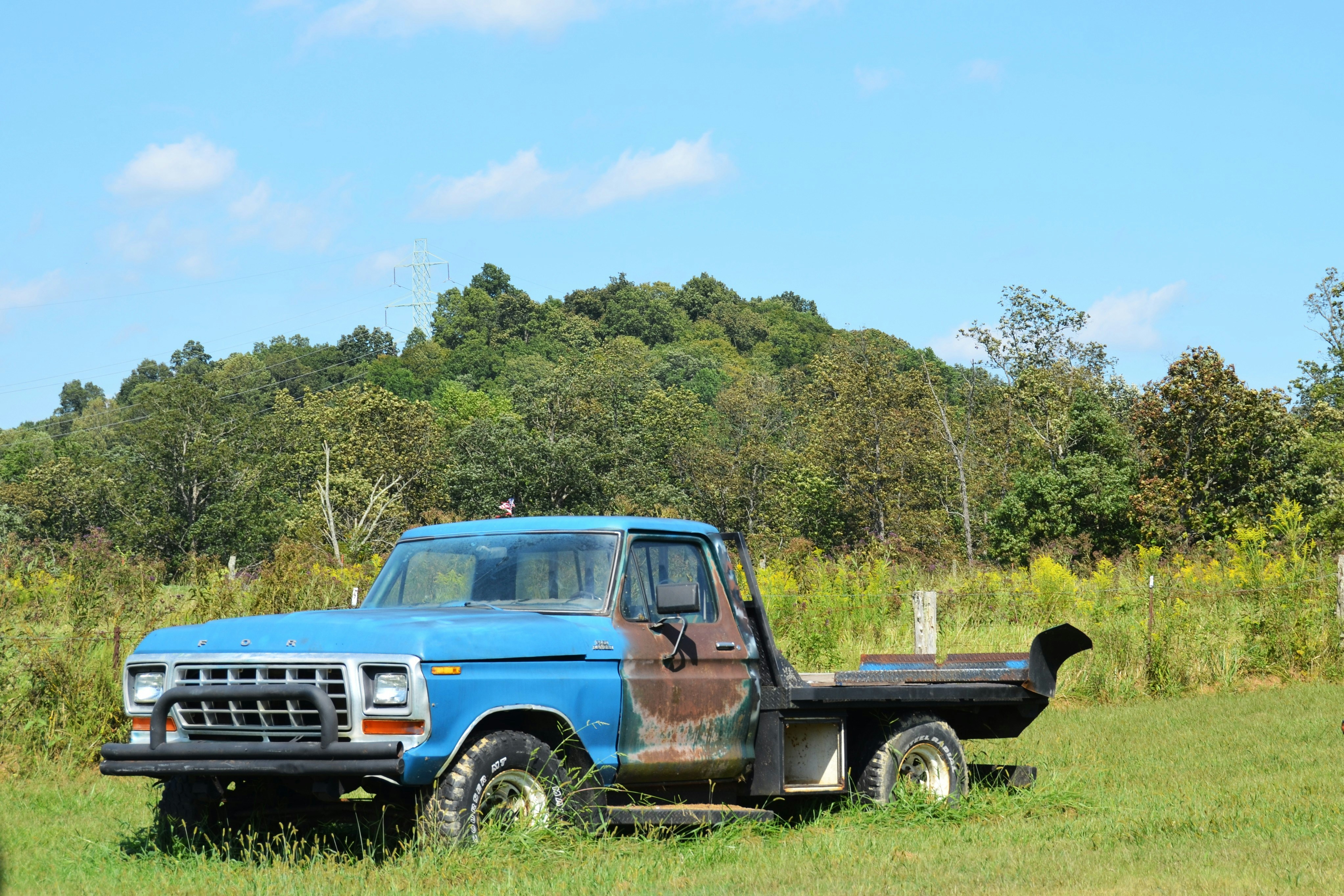 A weathered blue pickup rests under an open sky in a sunlit field