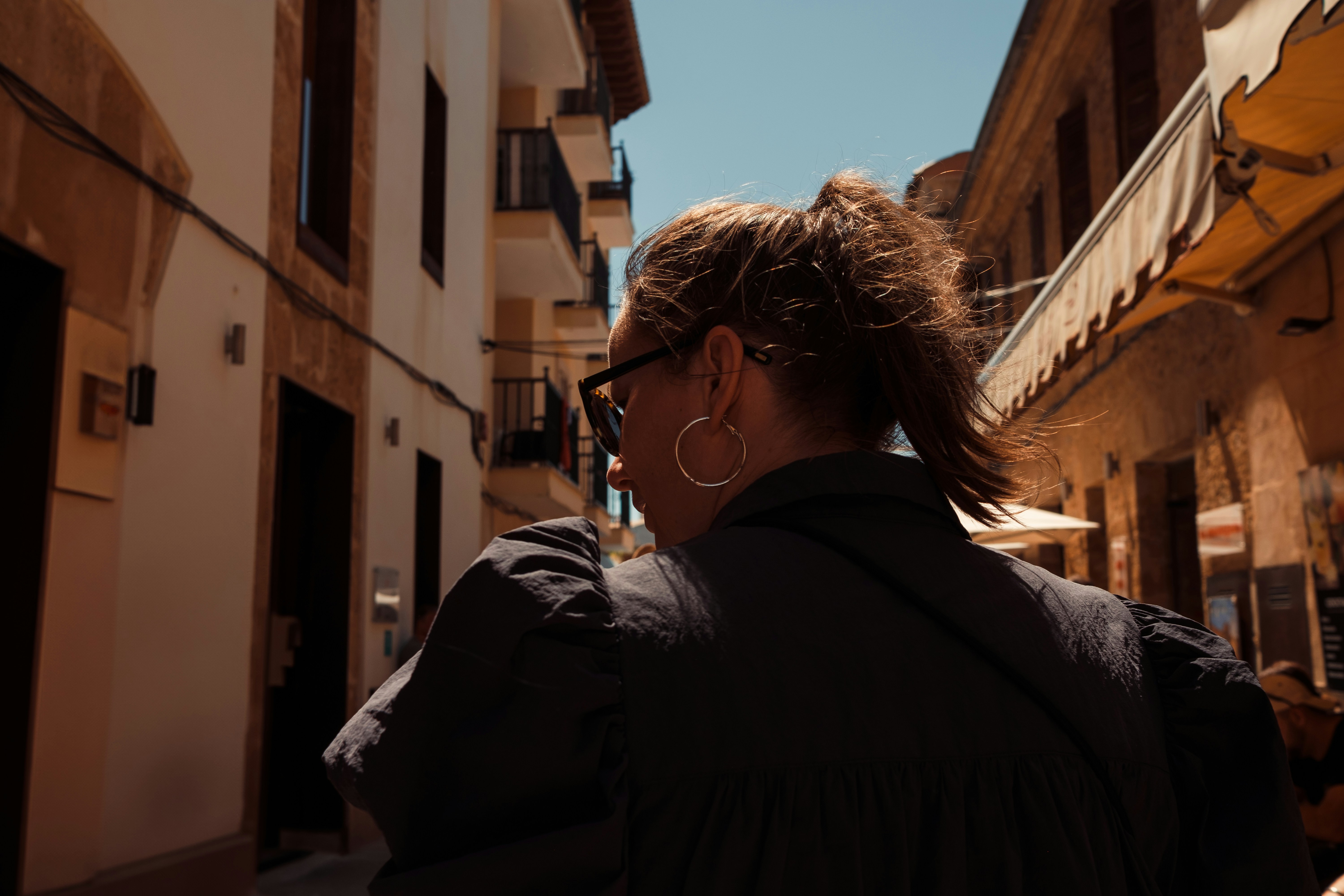 Backlit Street Portrait: A Woman in Dark Attire Walking Through Warm-Colored Alleys
