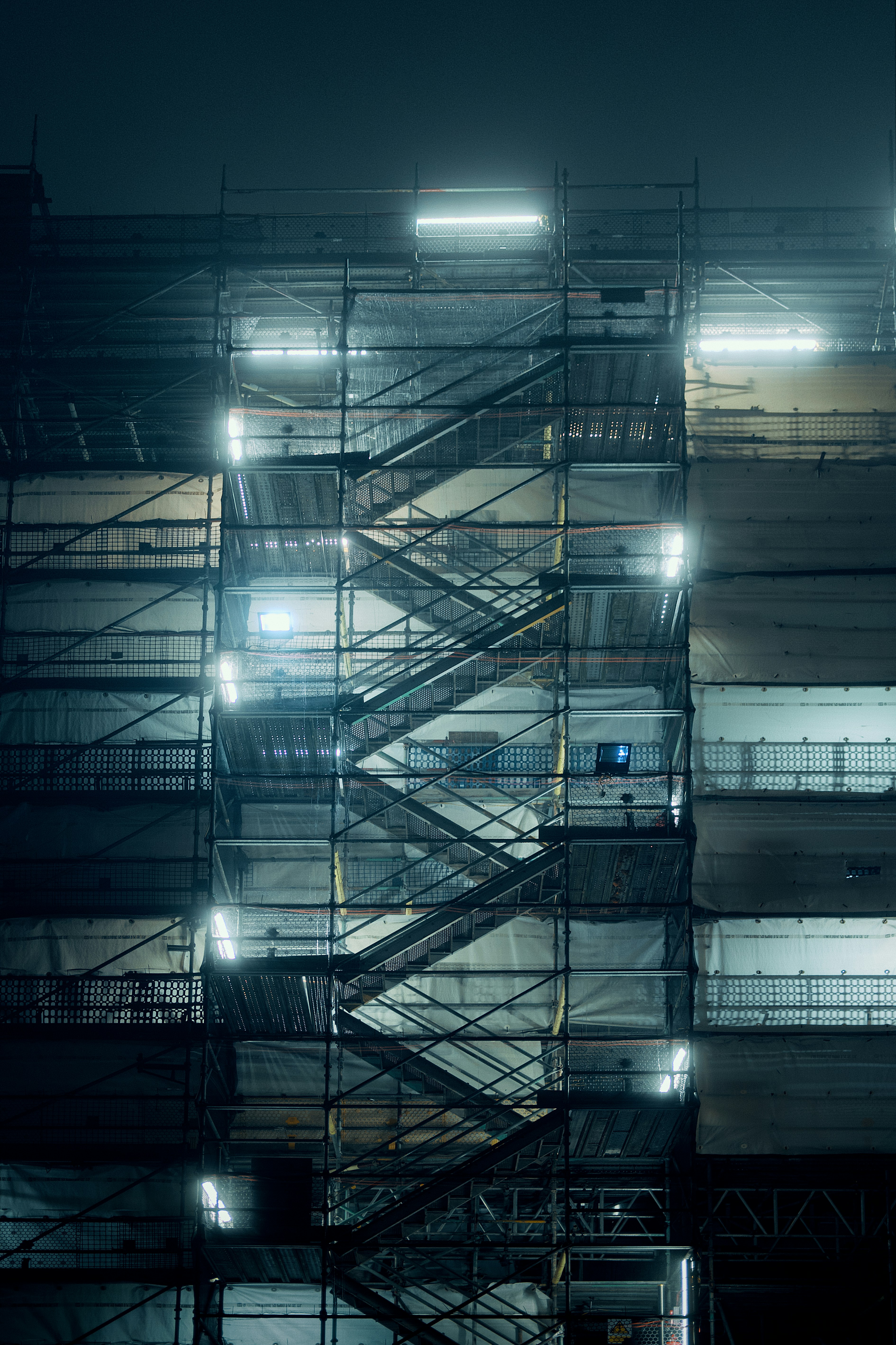 Neon-lit scaffolding ascends through a dim construction shaft