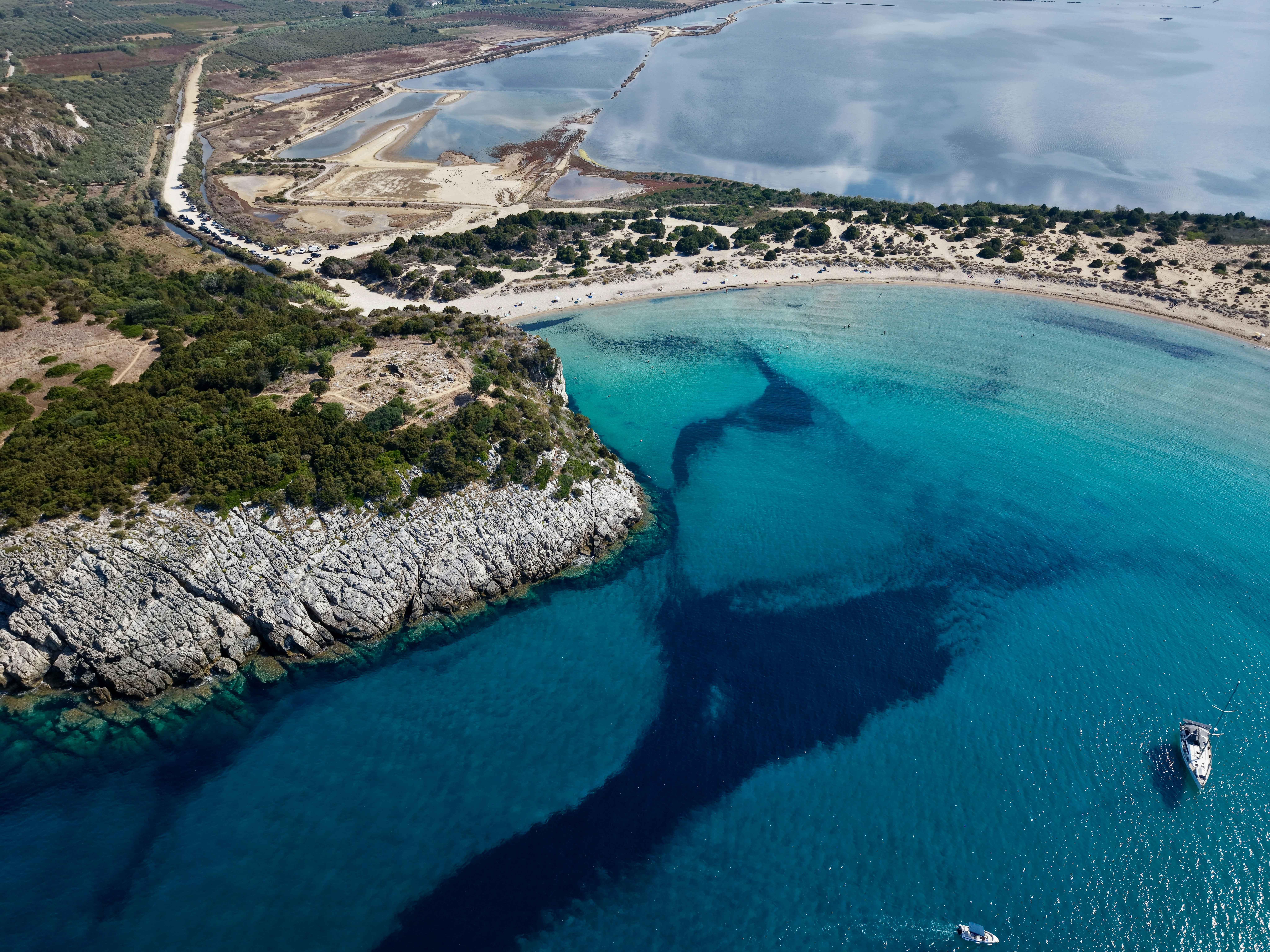 An aerial view of a turquoise bay with a rocky headland and sandy beach