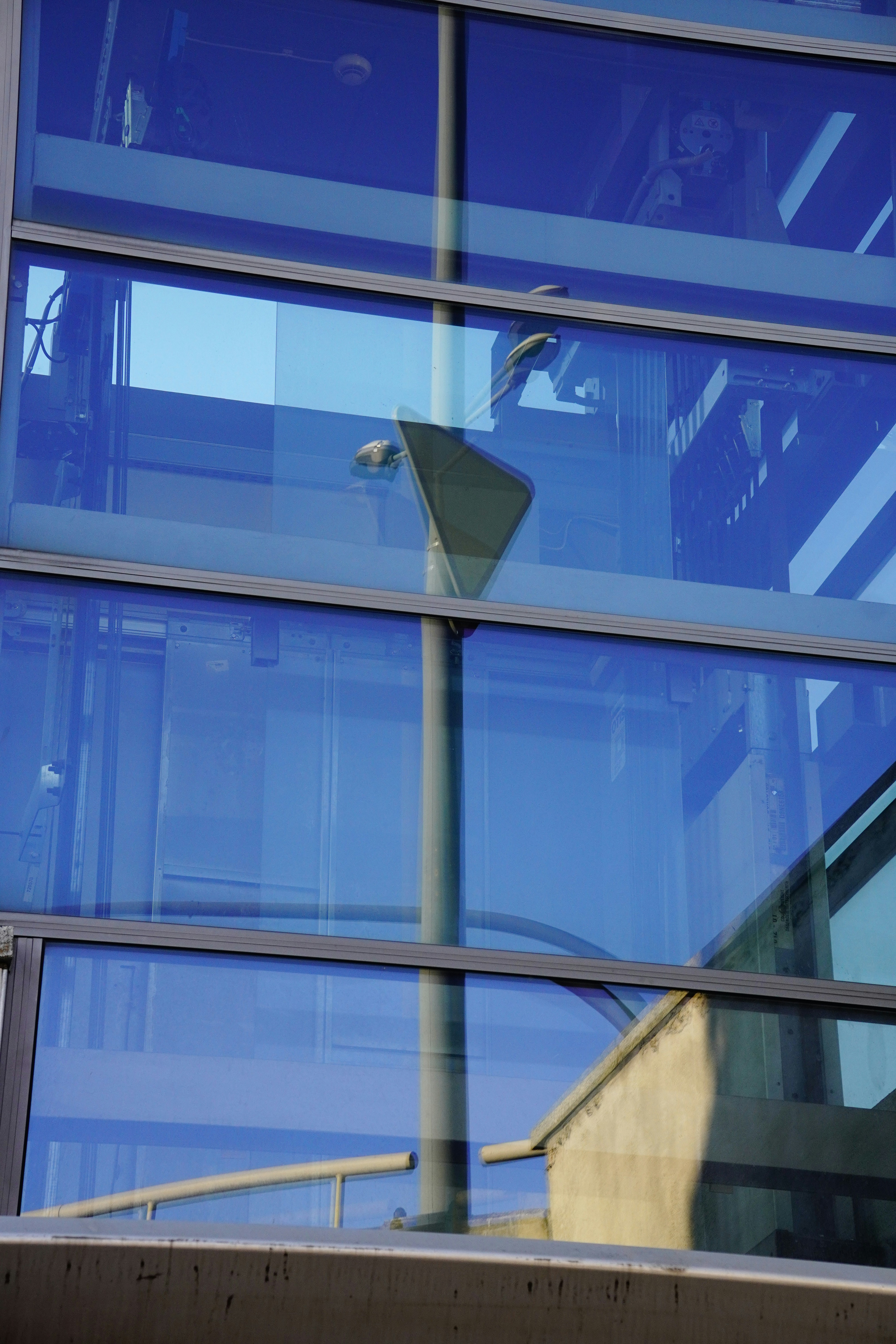 Reflections in Blue Glass: Street Lamp and Rails through Modern Facade