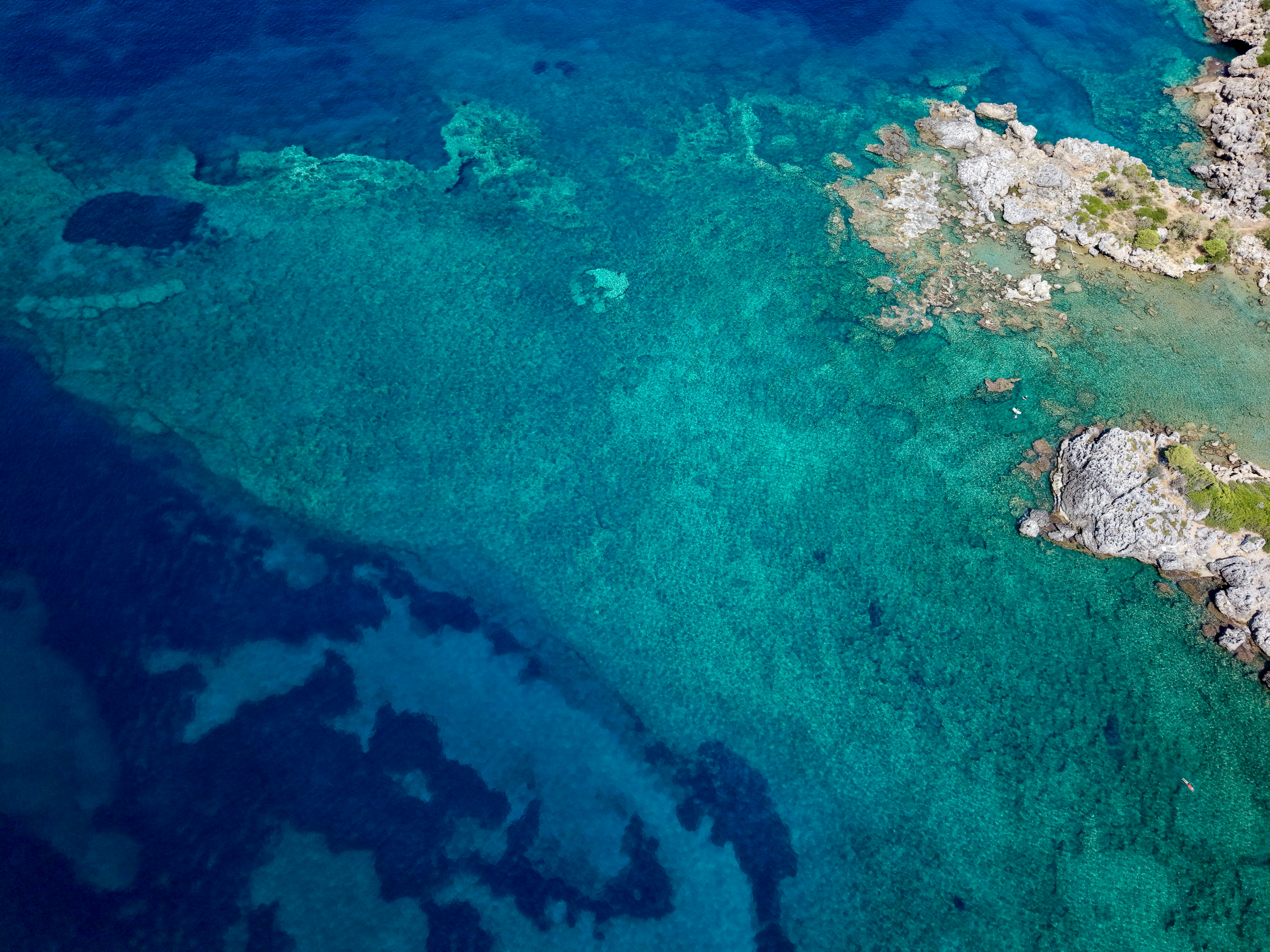 Aerial view of turquoise water meeting a rocky coastline with sparse green vegetation
