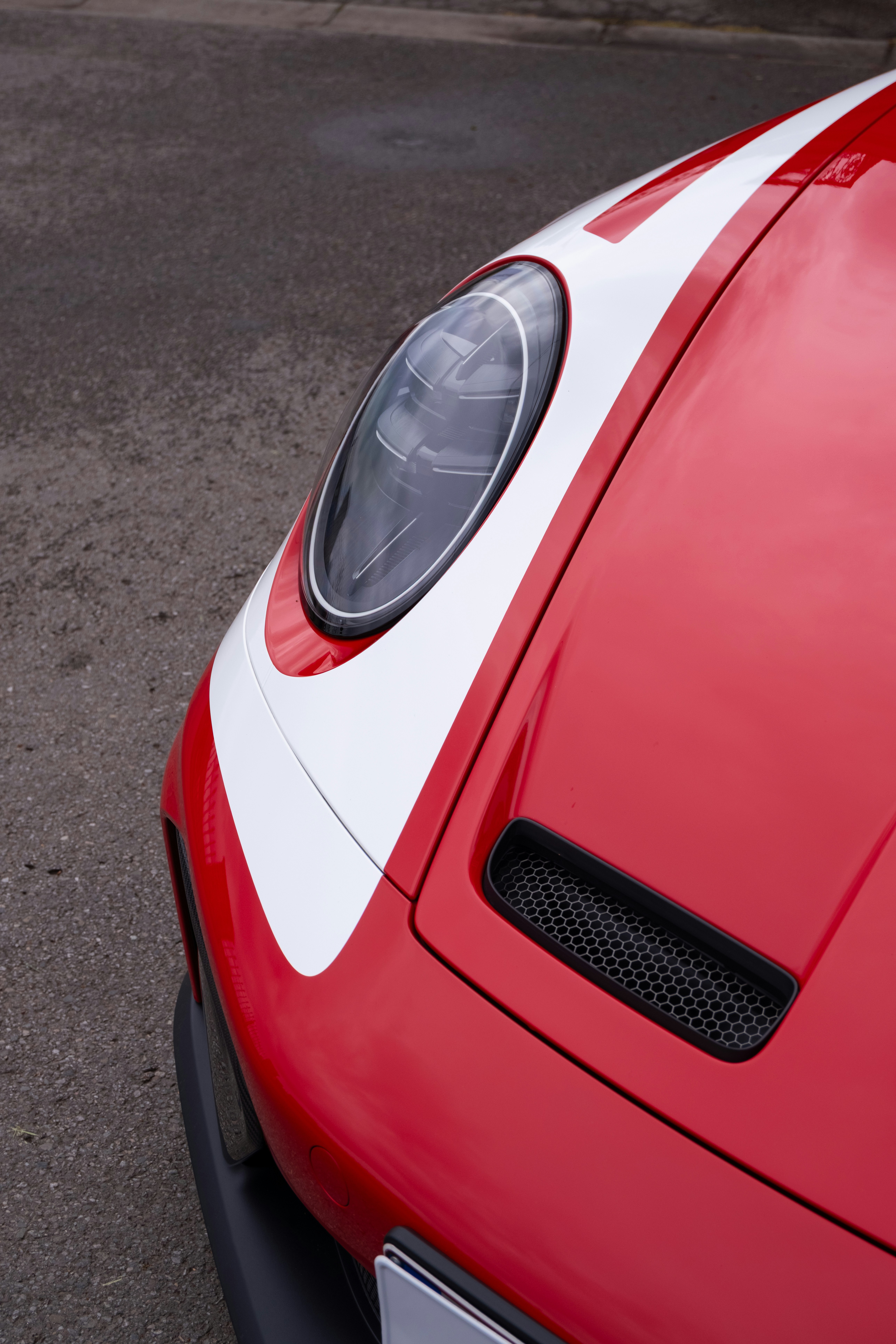 Red Porsche head-on curve: close crop reveals racecar’s eye-shaped headlamp and vented hood