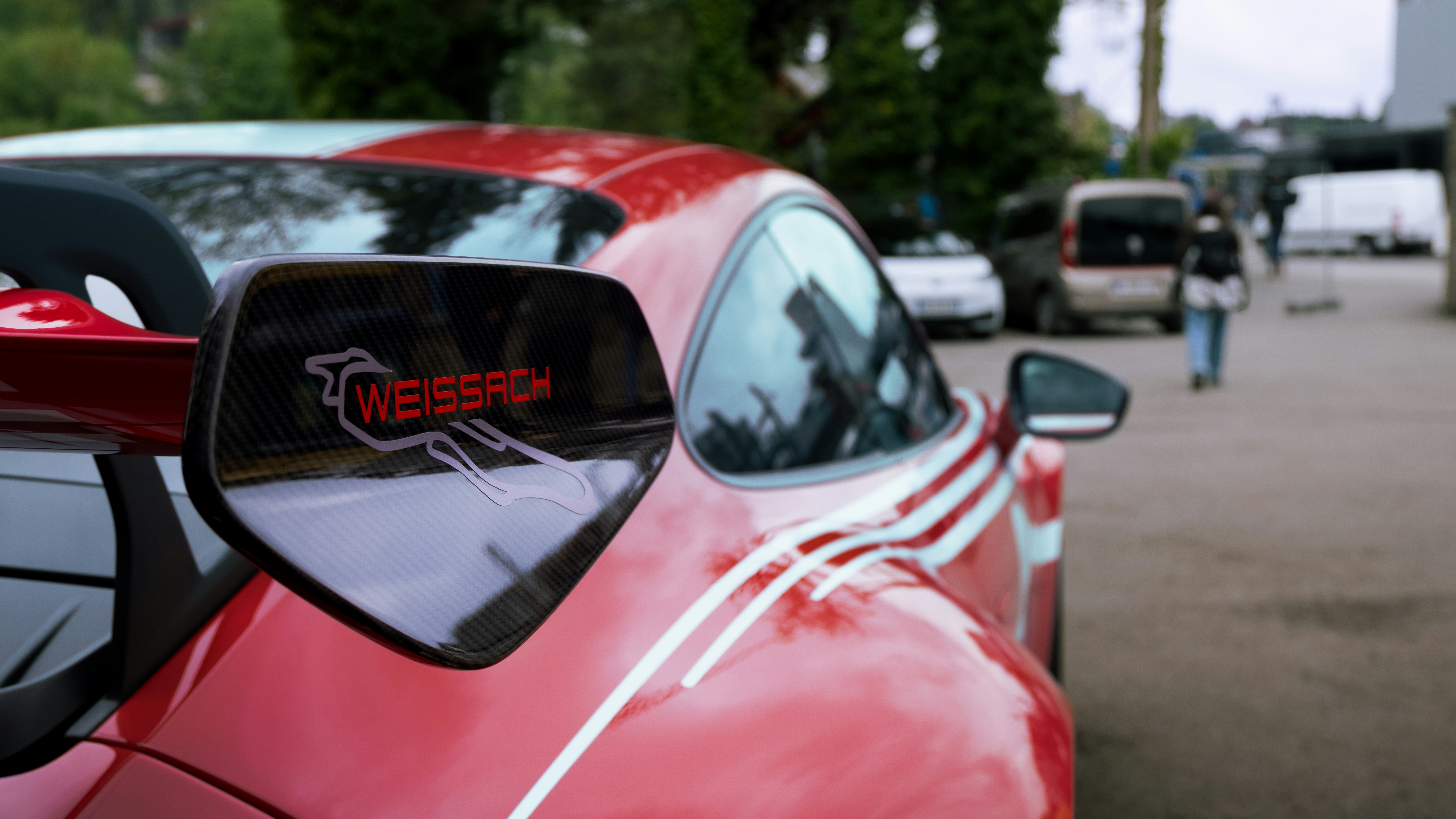 A red sports car with a carbon fiber wing reading Weissach in a parking lot
