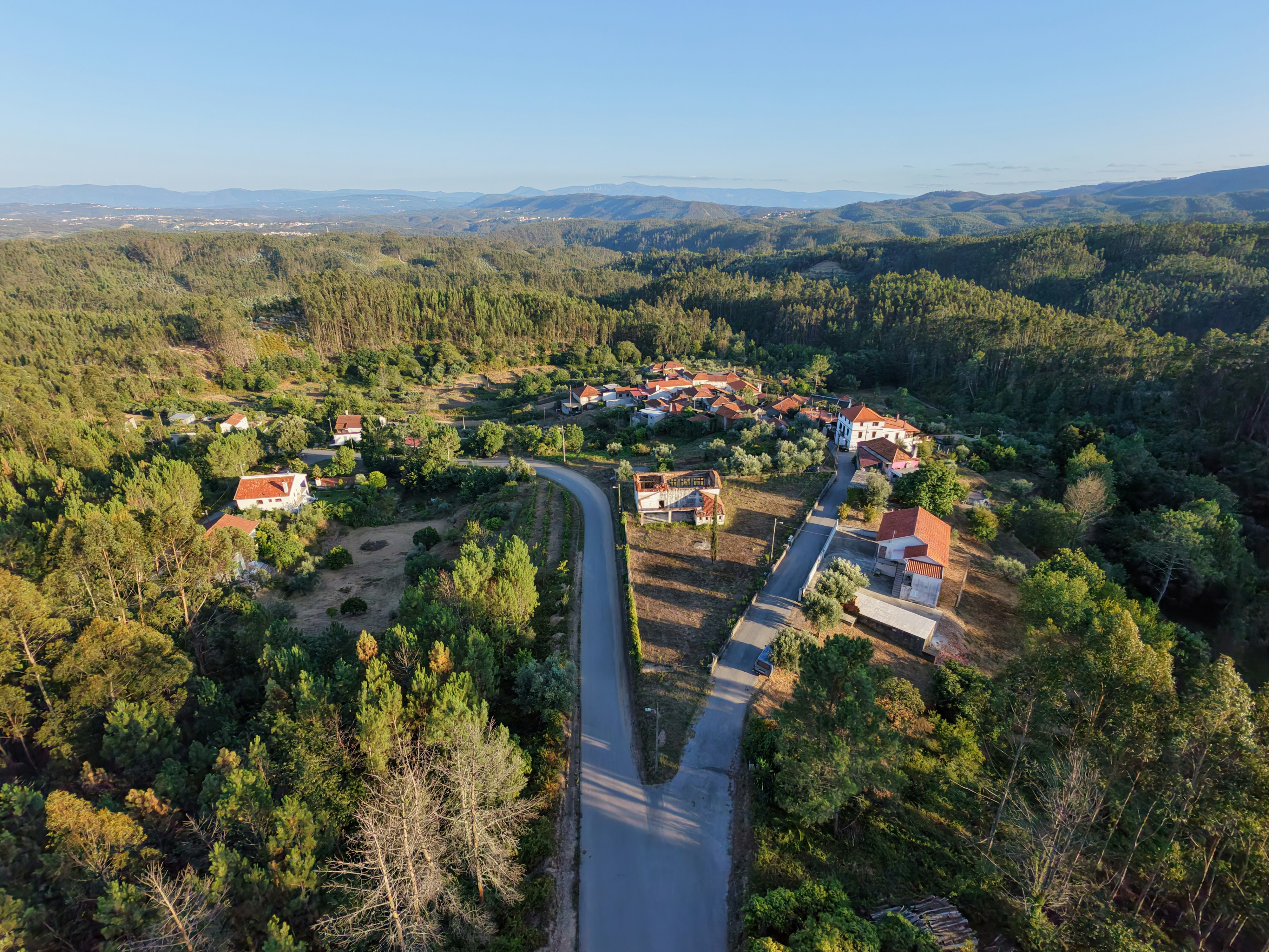 Aerial view of houses with red roofs and branching roads surrounded by forested hills.