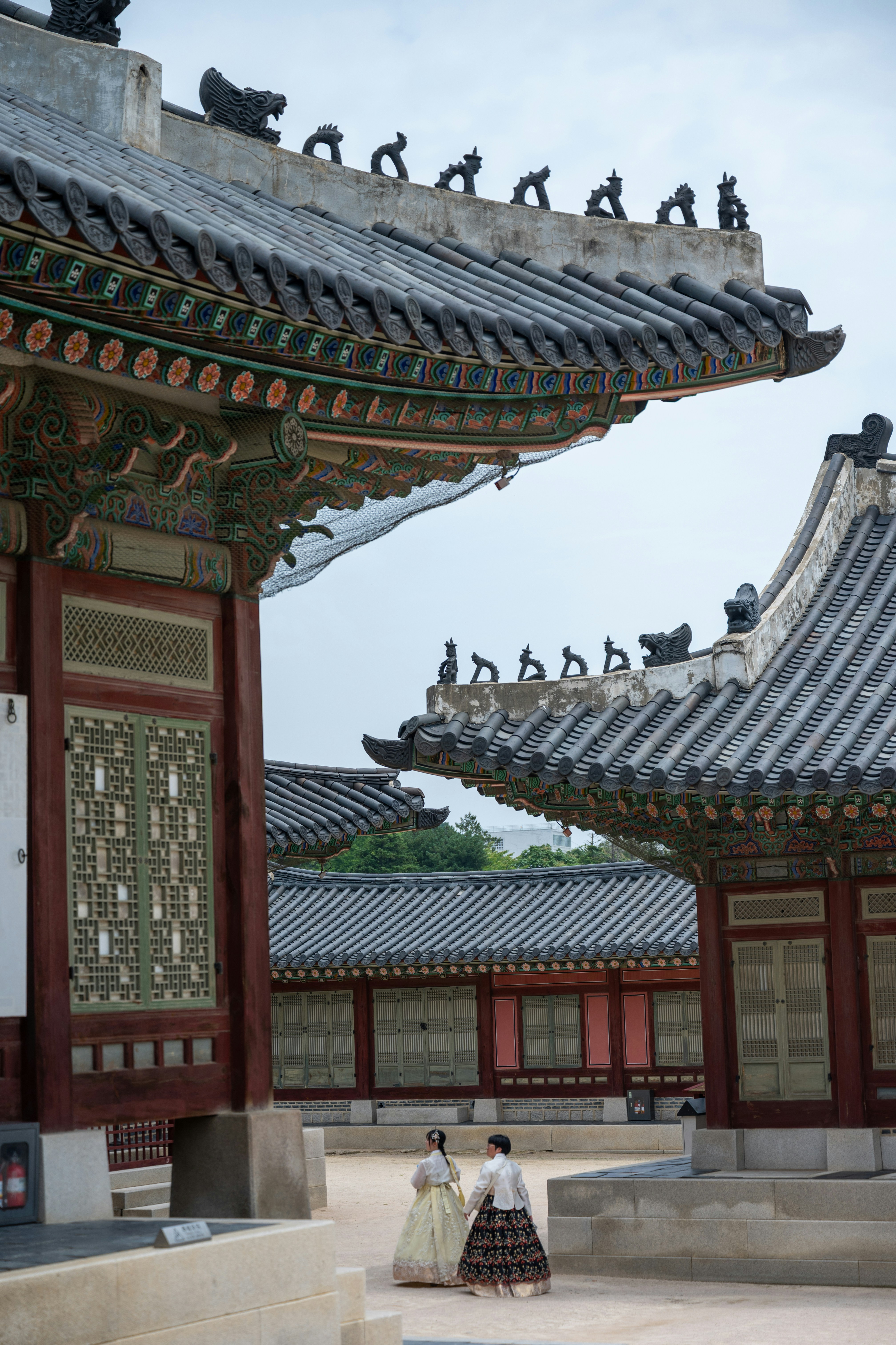 Courtyard Echoes: A Pair in Traditional Hanbok Between Timeworn Rooflines