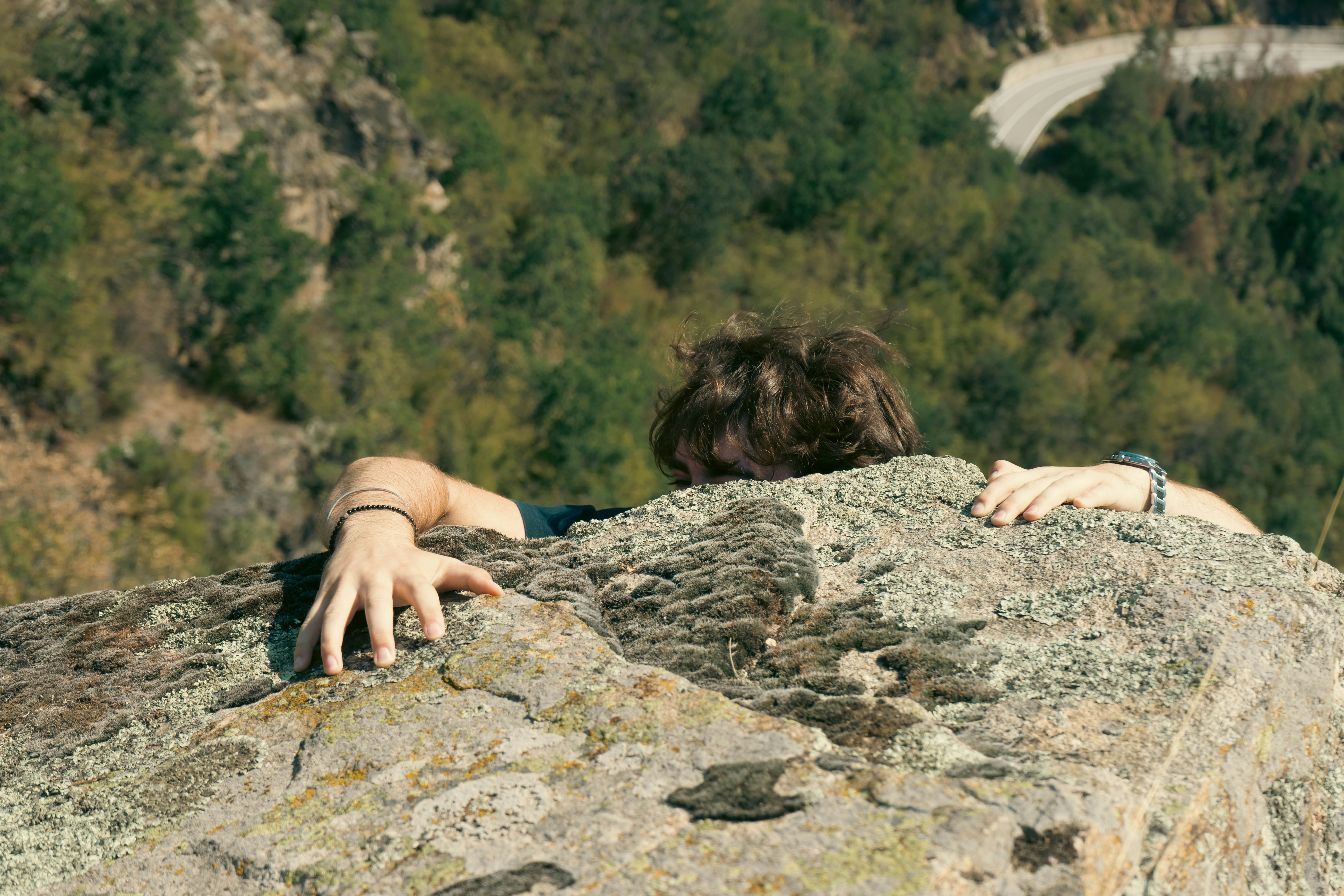 Cliff Hanger: Hands Gripping the Rock Over a Forested Drop