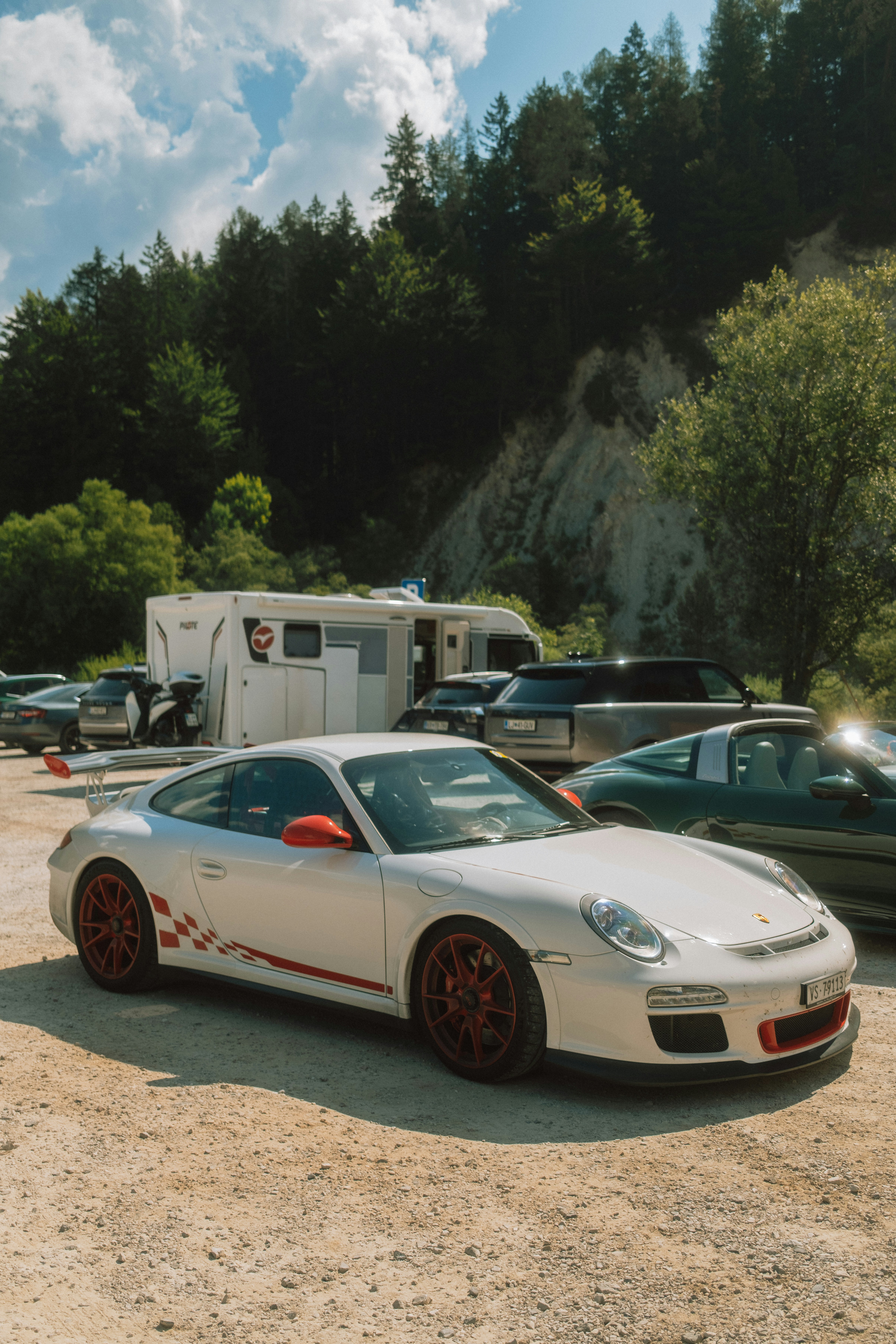 White Porsche Rally Car in Gravel Lot with Backdrop of RV and Forest