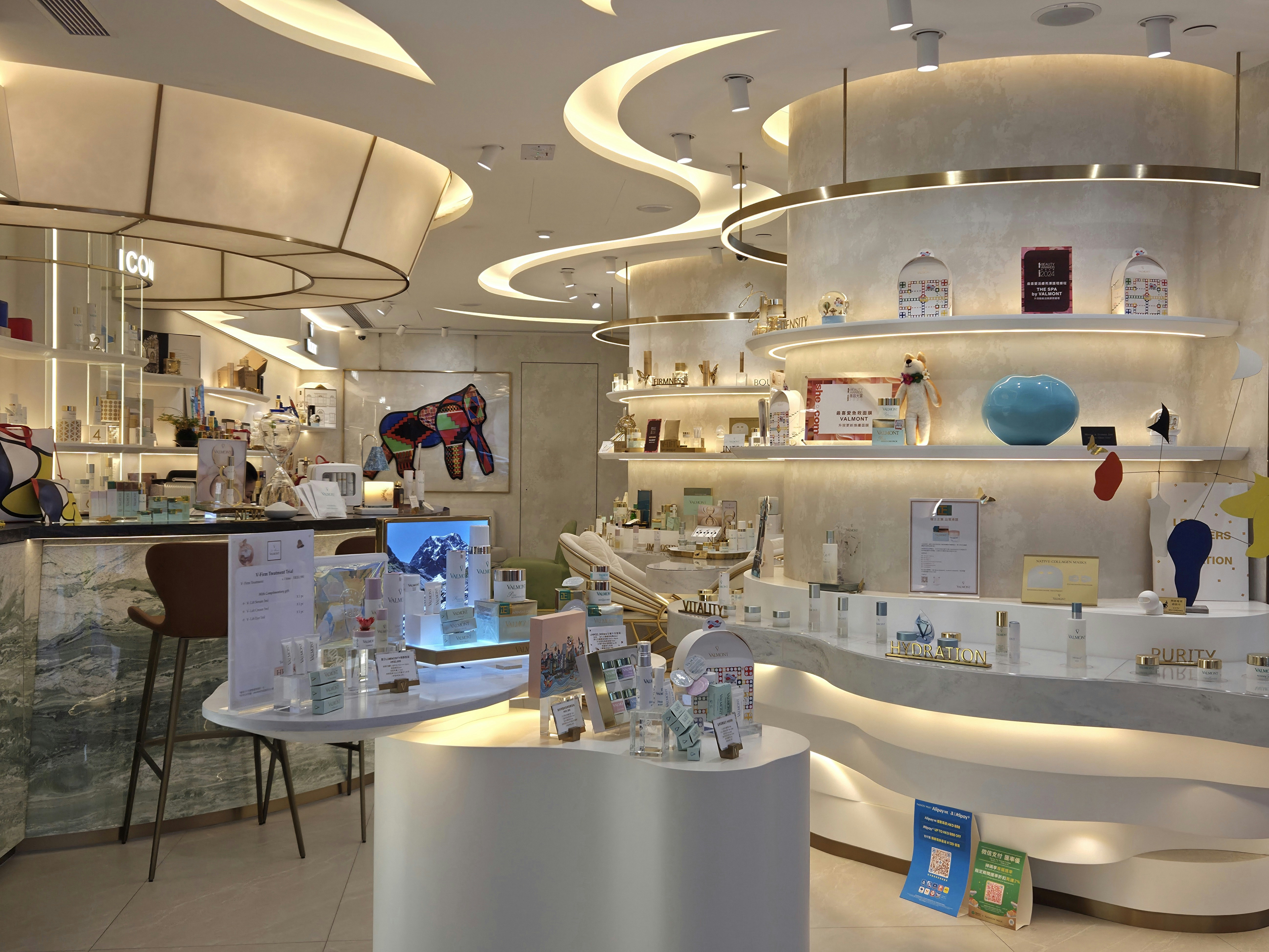 Bright showroom with curved ceiling lighting and white shelving, featuring products and a few display stands; a modern retail space with soft, warm illumination.
