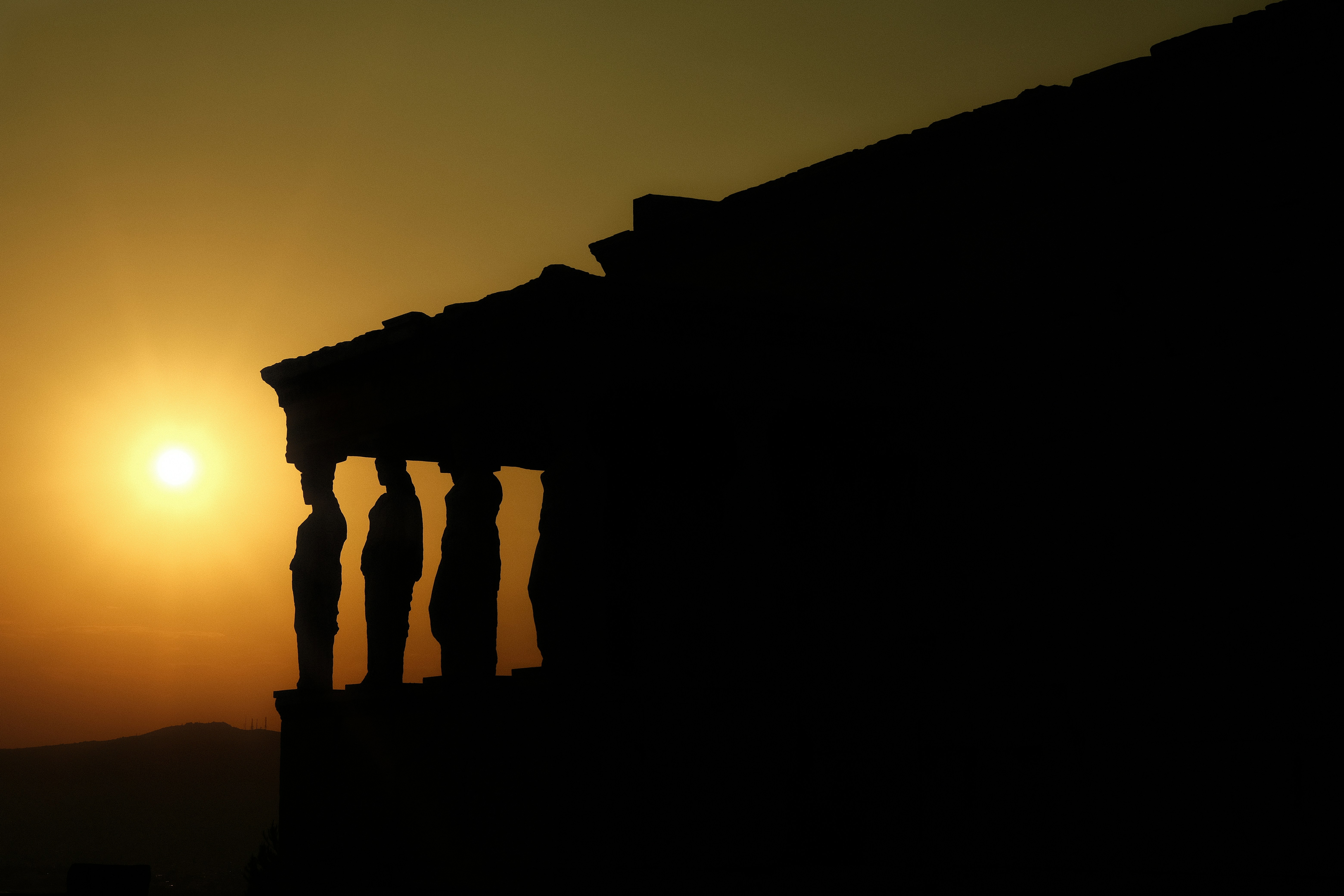 Silhouette of an ancient columned ruin against a rising sun