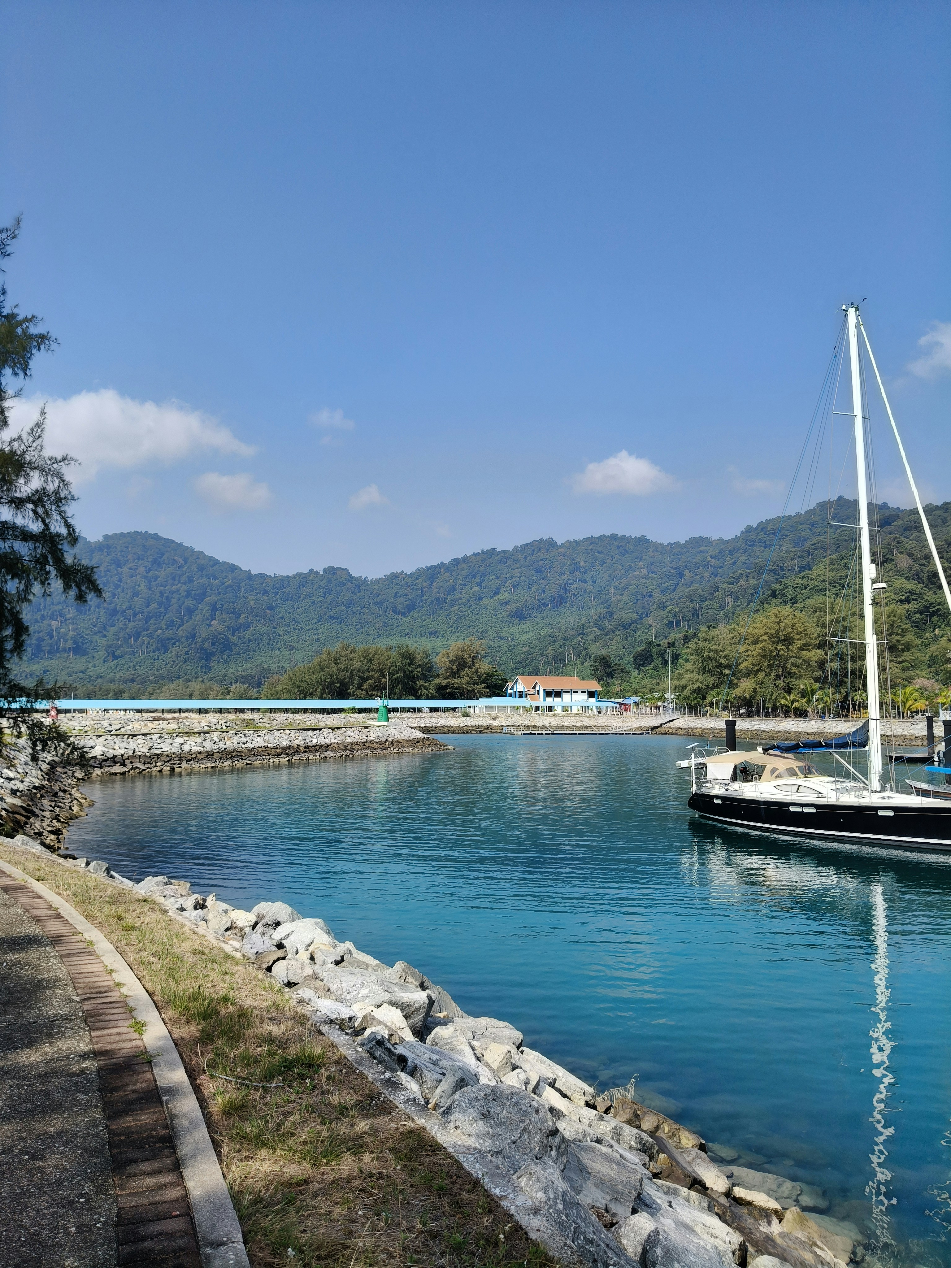 A sailboat moored in a calm blue harbor with forested mountains in the background
