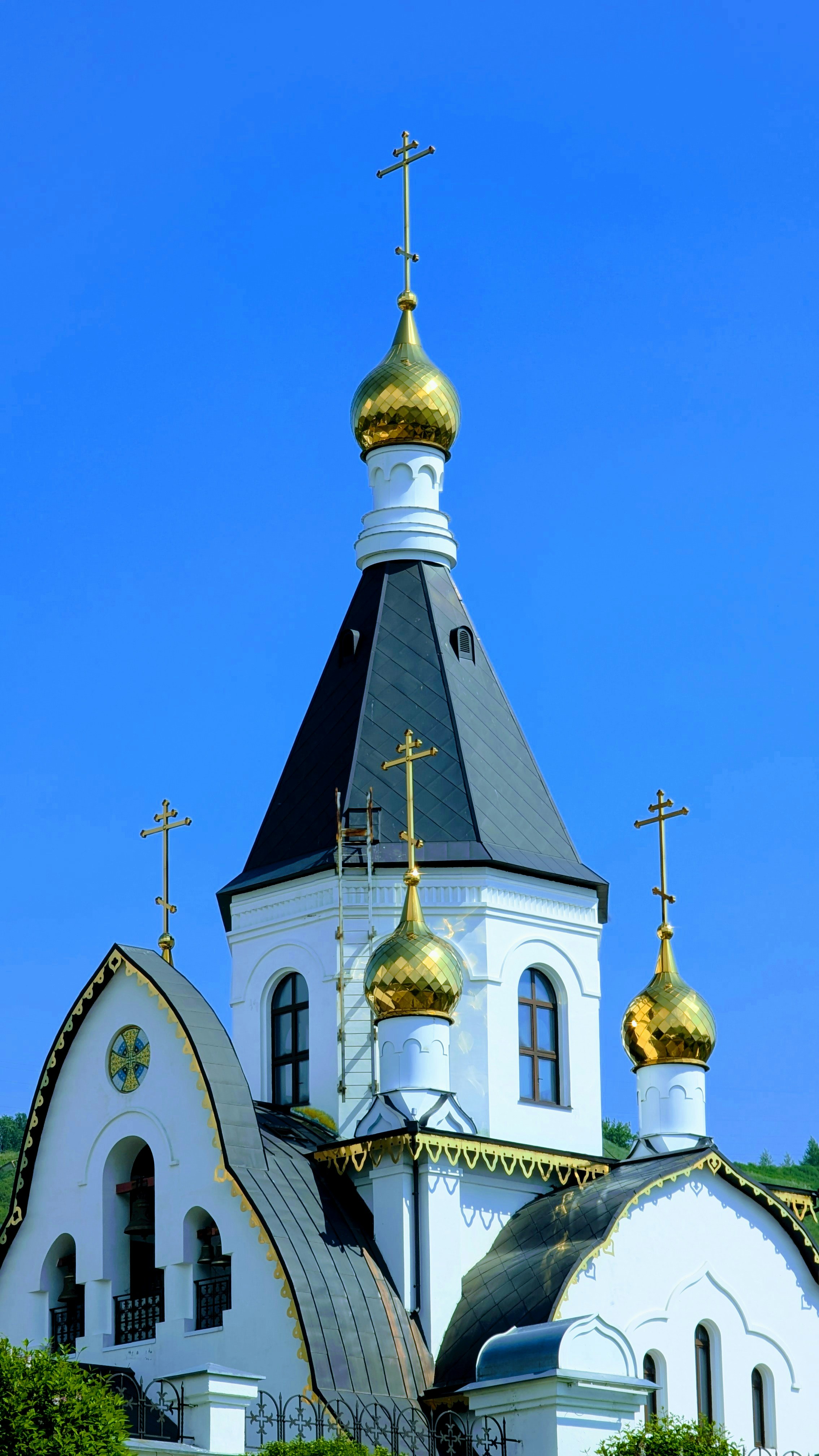 White church with golden onion domes and dark roof set against a vibrant blue sky; architectural details and crosses emphasized.