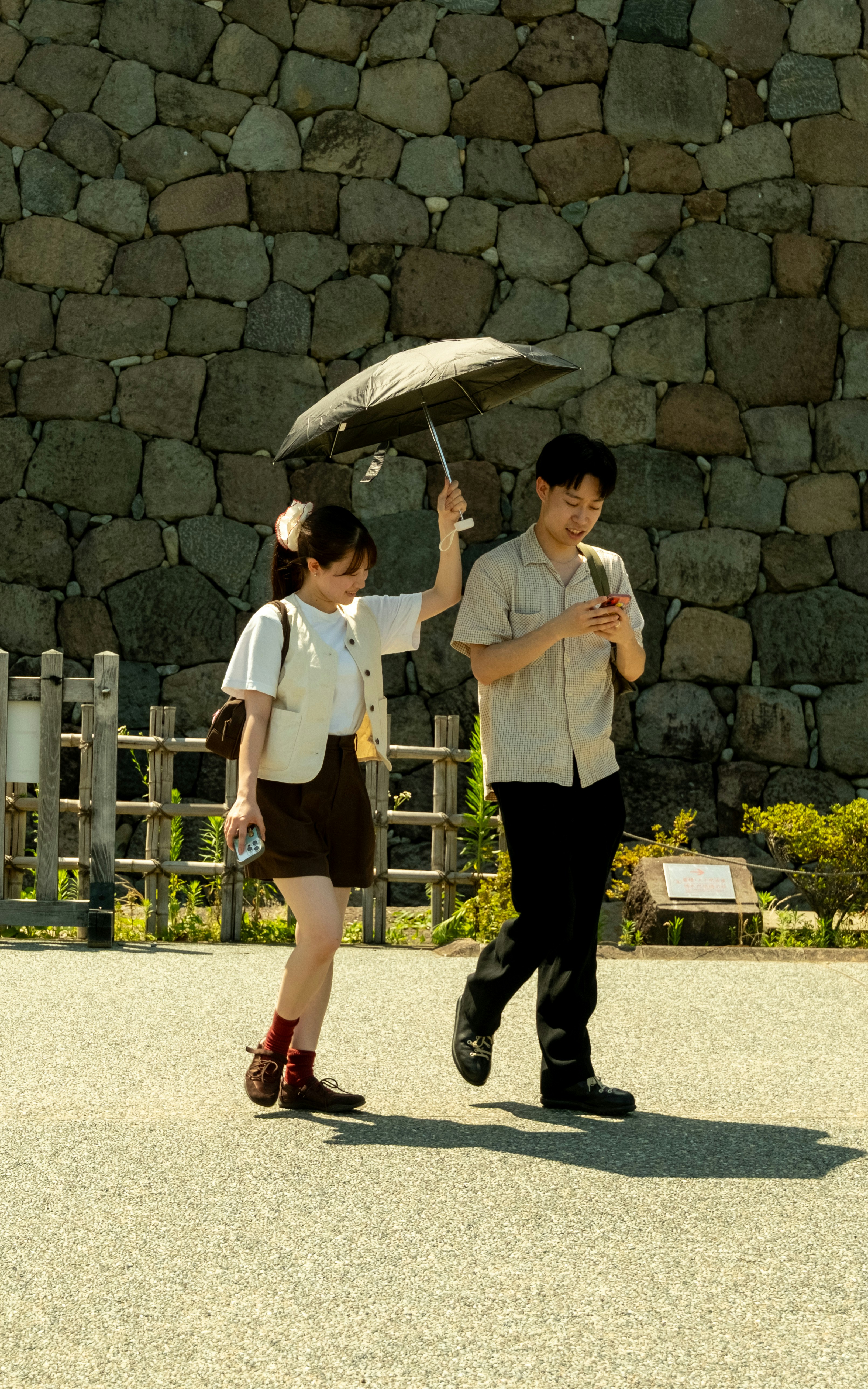 Sunlit stroll under an umbrella: a candid moment by the stone wall