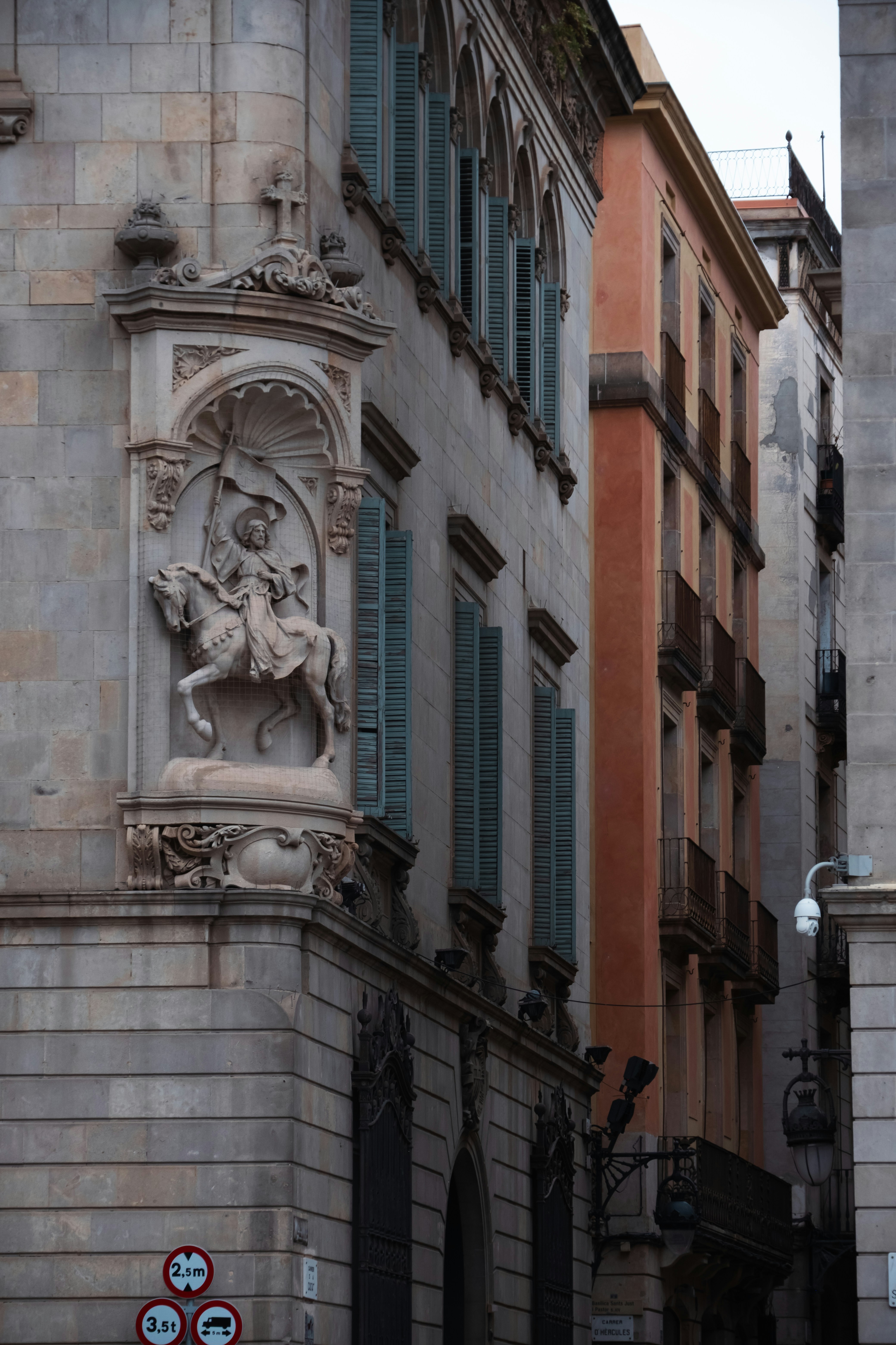 Carved Hero on a Historic Façade: Stone Relief Overlooked by Narrow Street