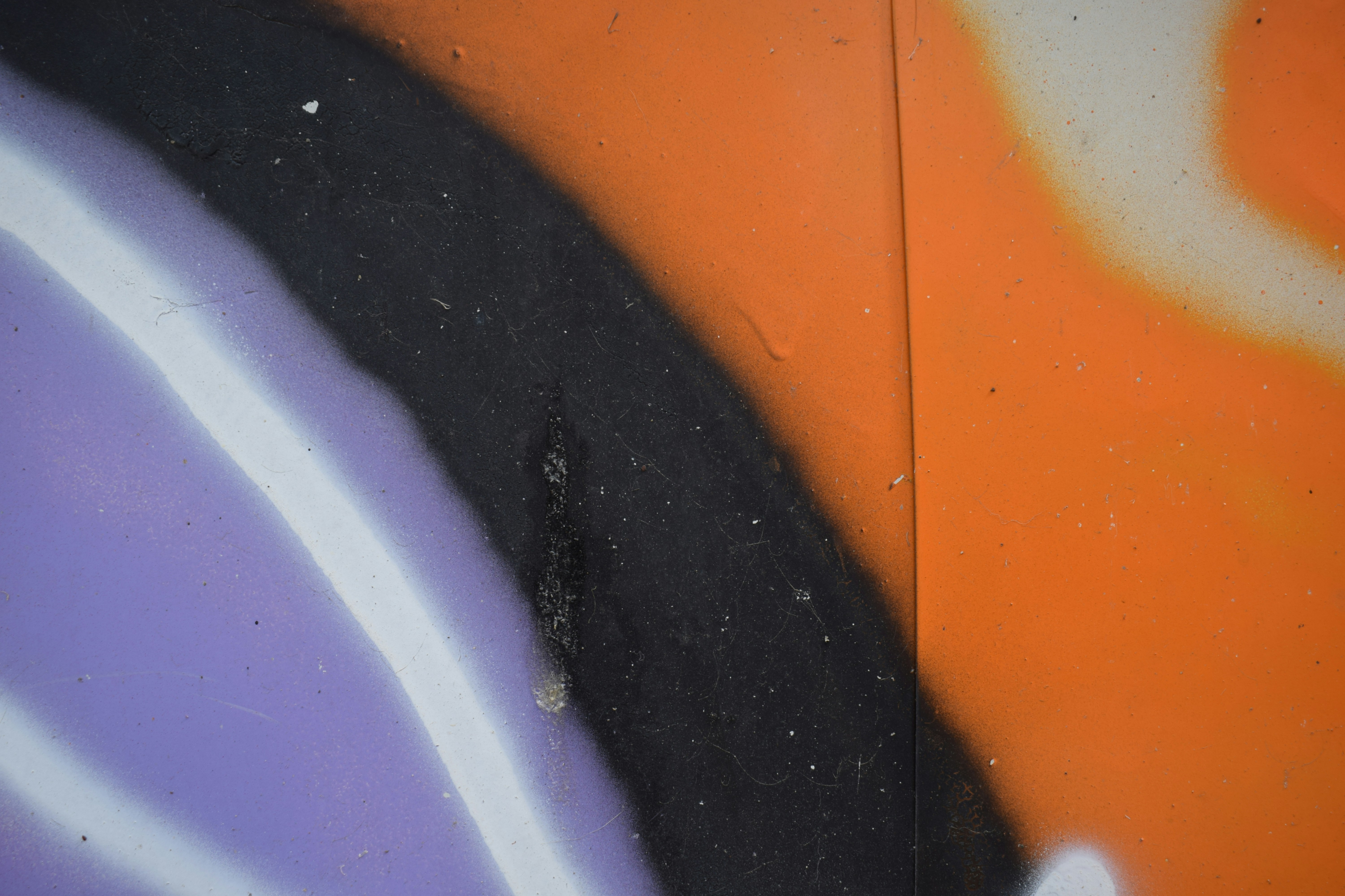 Close-up of vibrant graffiti with bold orange and purple shapes separated by a sharp seam; the image emphasizes color blocks and texture in an urban wall detail.