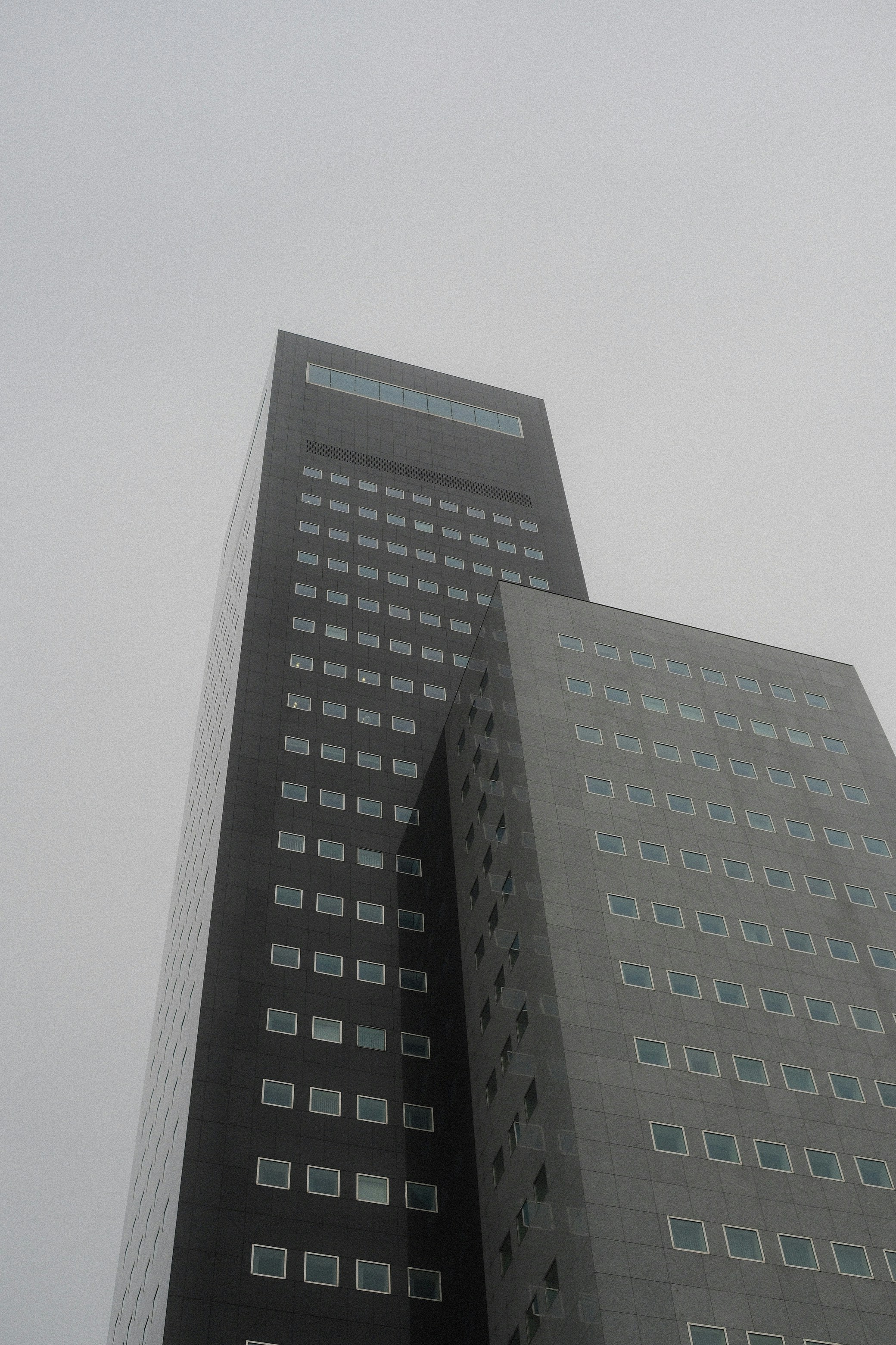 Tall, modern office towers loom diagonally with grid-patterned windows in muted gray, set against a pale overcast sky.