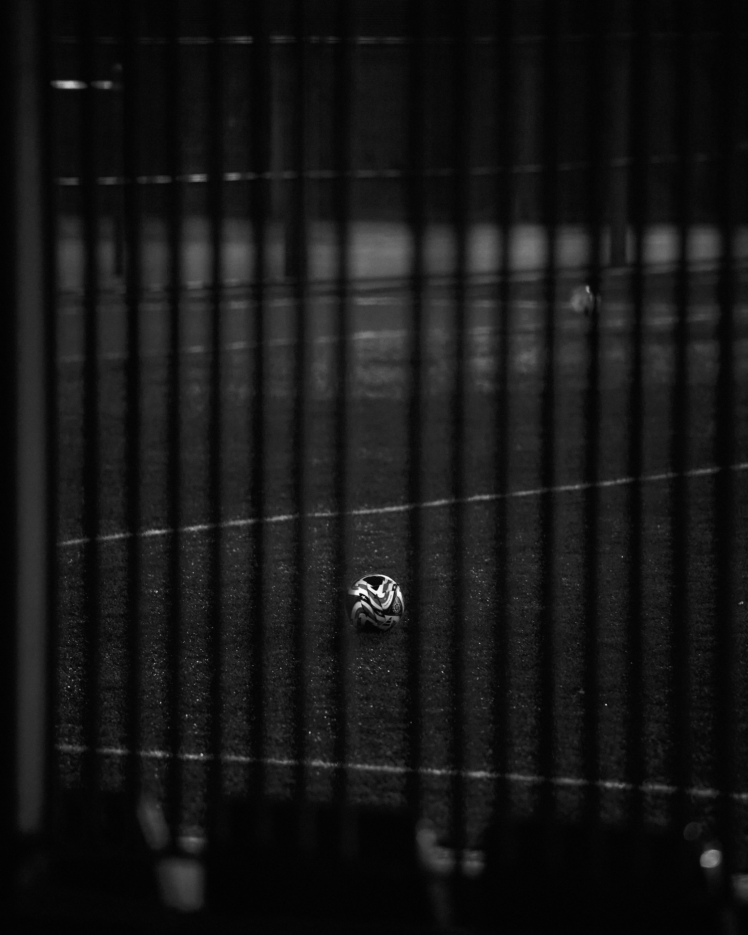 Forgotten Ball on a Rainy Field Behind Bars