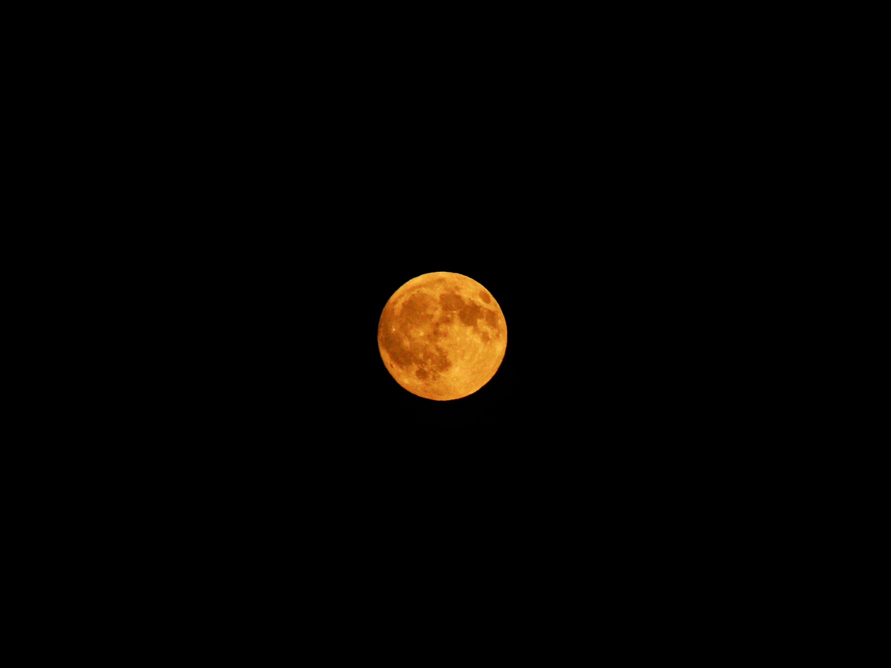 Bright orange full moon against a dark sky, centered with crisp lunar details and subtle atmospheric texture.
