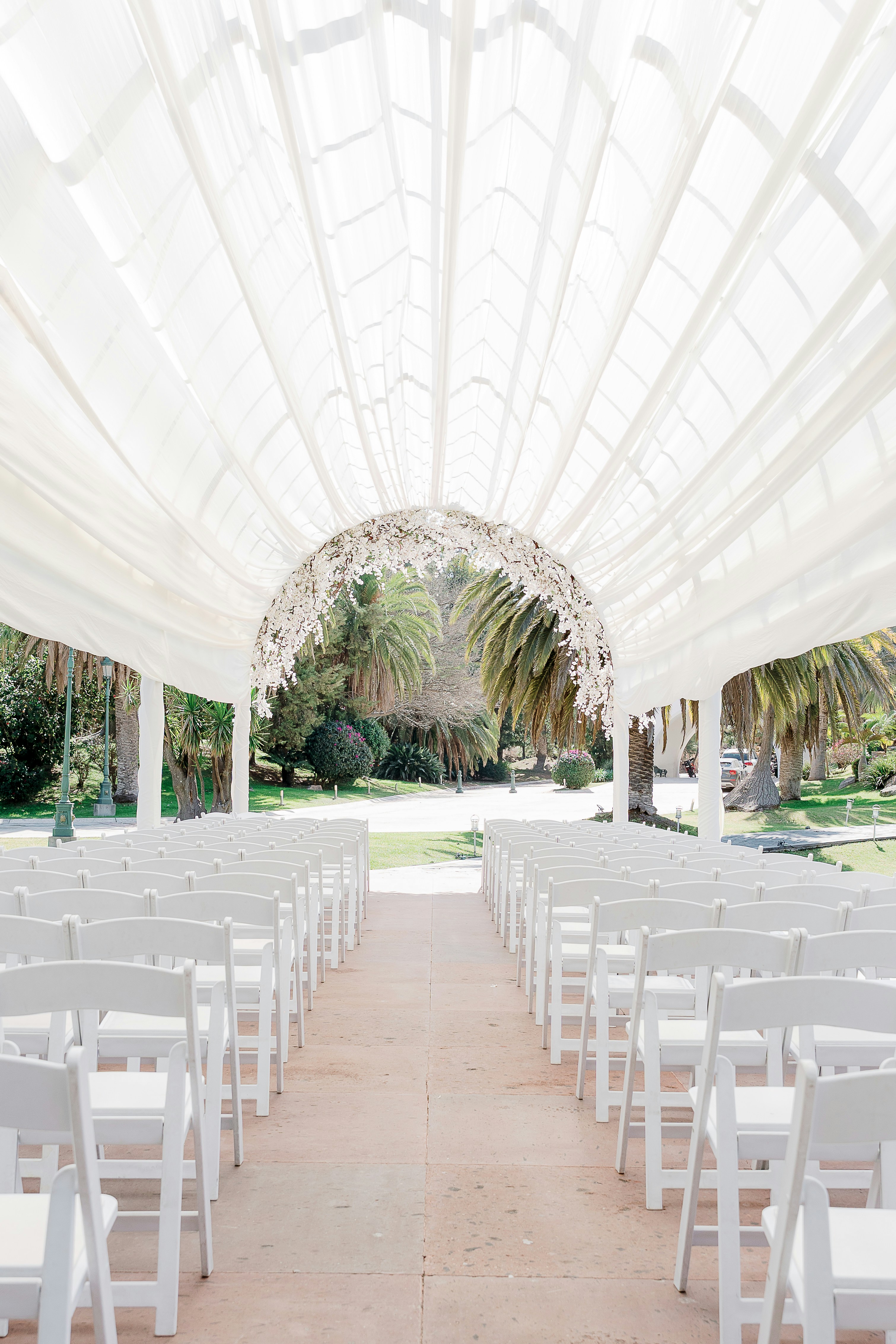 Rows of white folding chairs facing a floral arch under a draped canopy