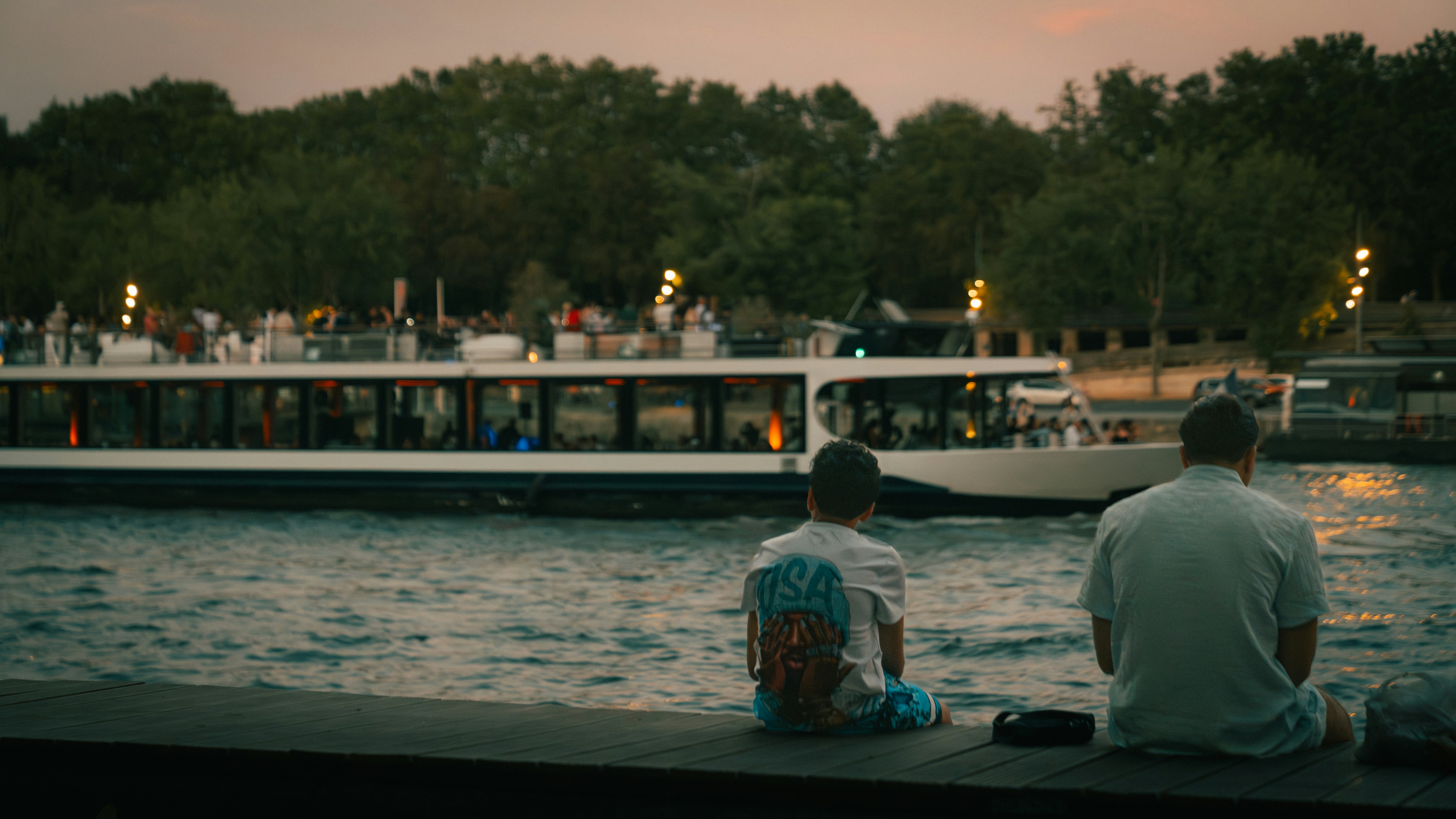 Two silhouettes by the riverwatching a passing boat at sunset
