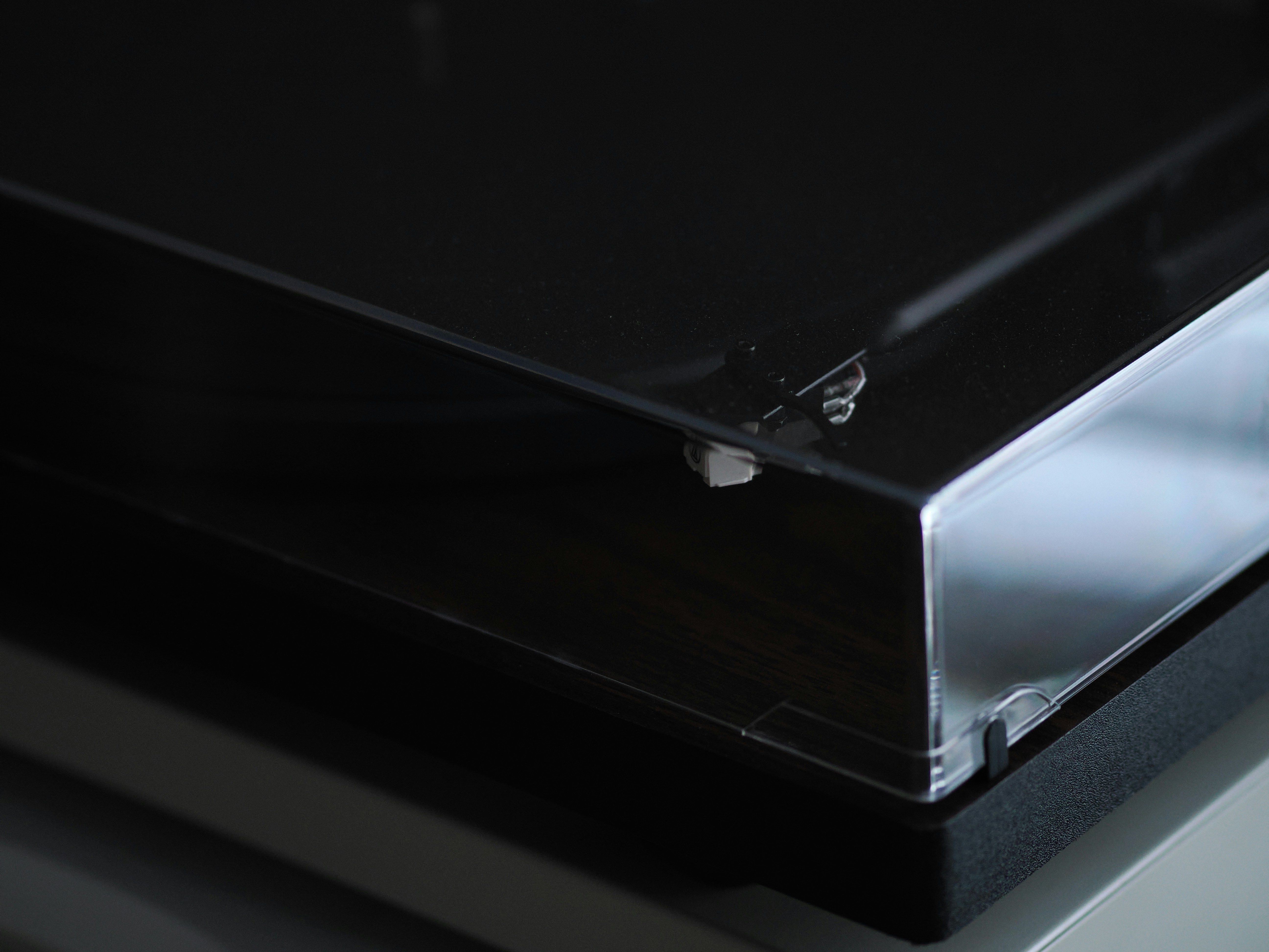 Close-up of a glossy black surface meeting a chrome edge with small hardware visible; a minimal, industrial detail shot. This is a macro-like still of a hardware edge, possibly part of a device or case.