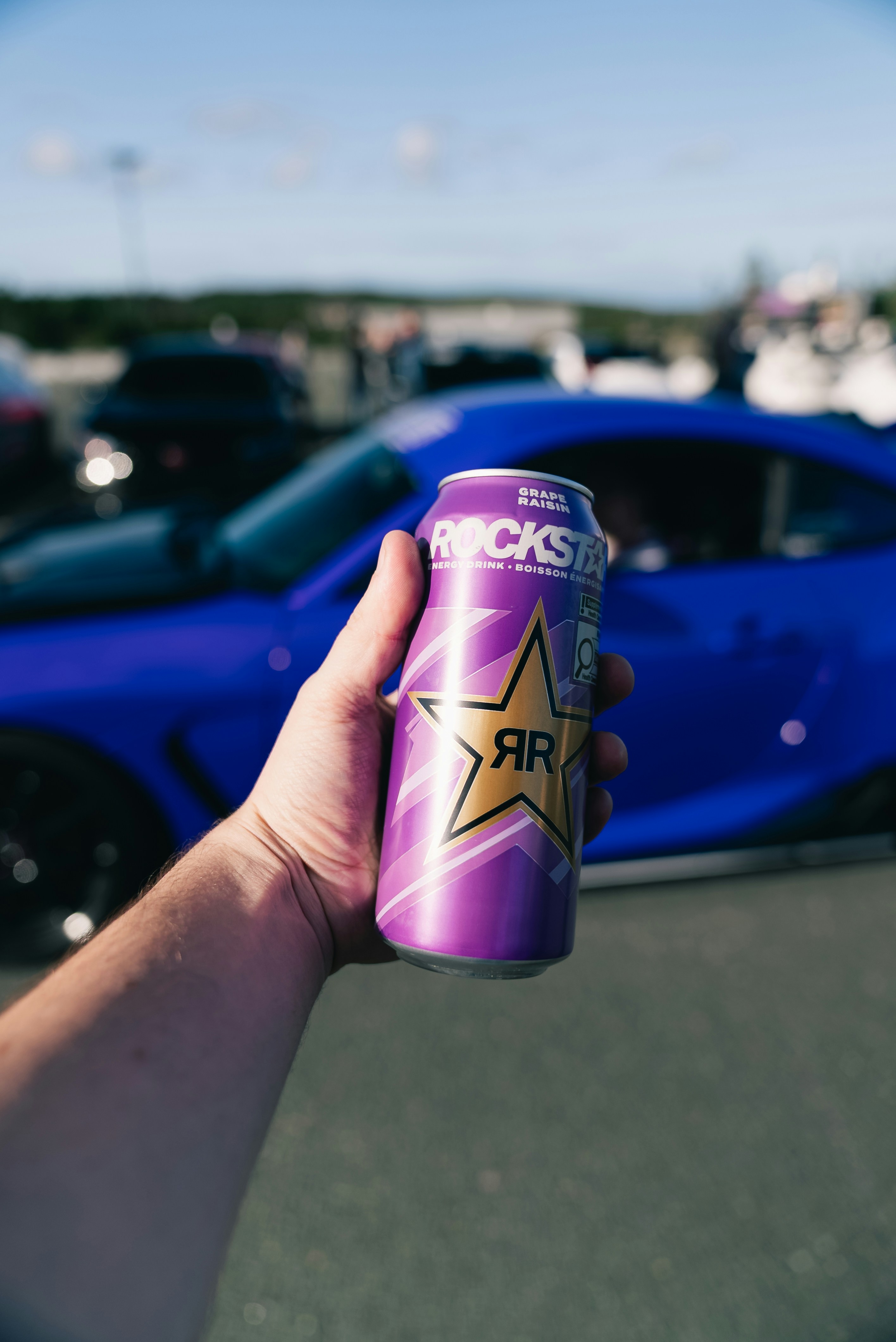 Purple Rockstar Can in Hand, Blue Car Backdrop in a Car Show
