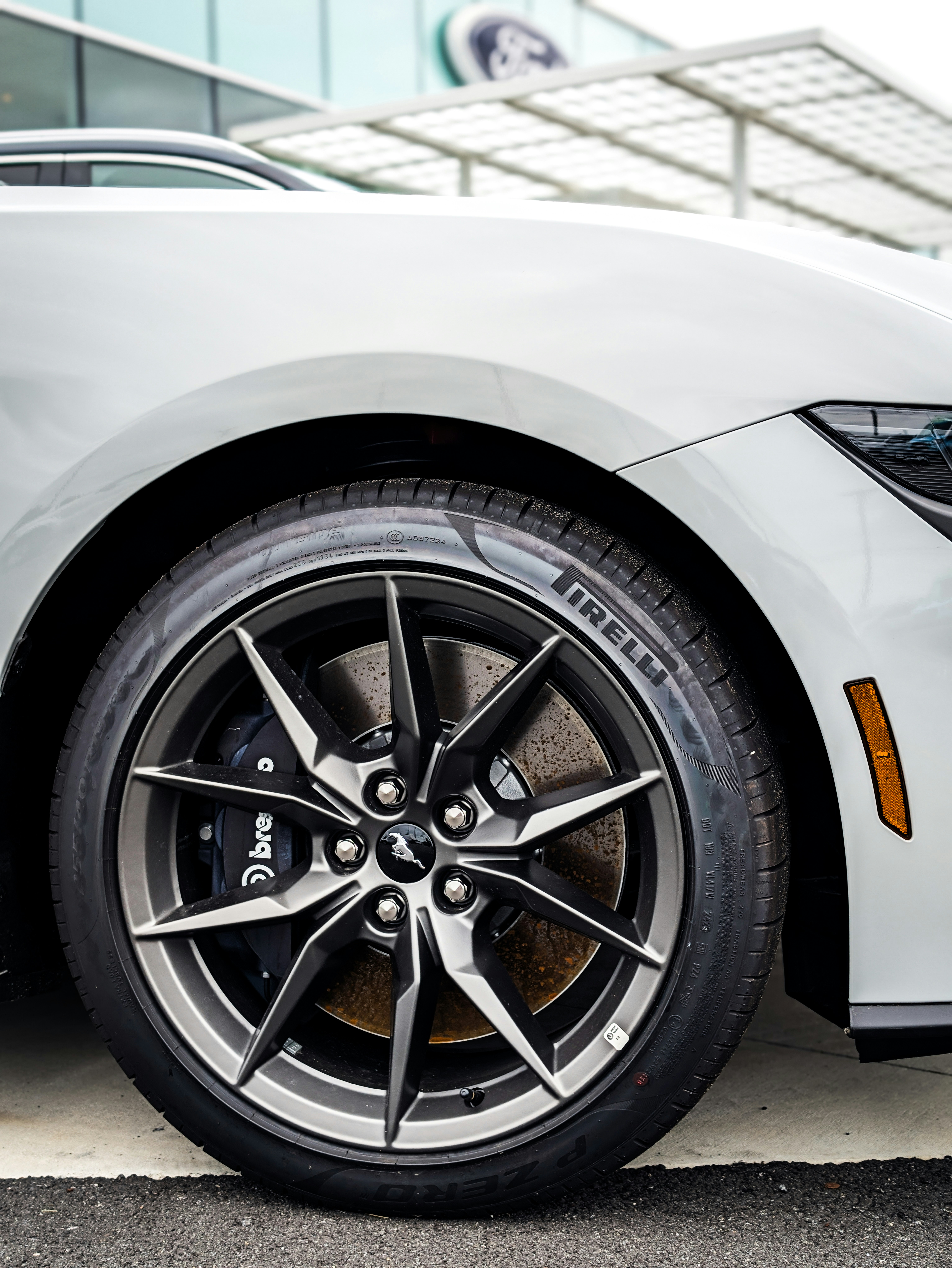 A pristine gray sports car reveals a dark alloy wheel wrapped in premium Pirelli rubber, showcasing a massive Brembo brake caliper over a rusted iron rotor on the paved asphalt.