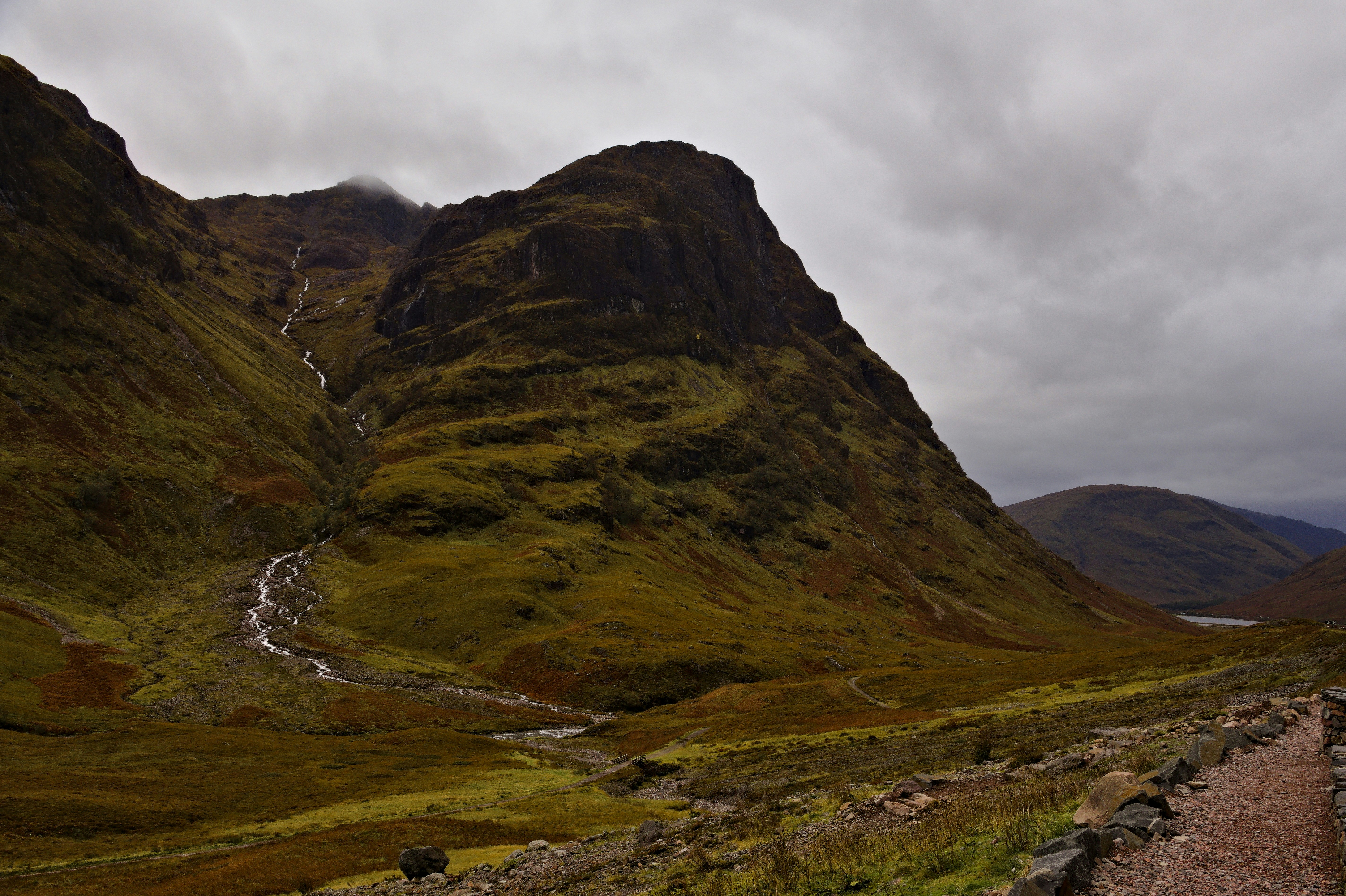 Moss‑clad peak under stormy skies with a winding stream