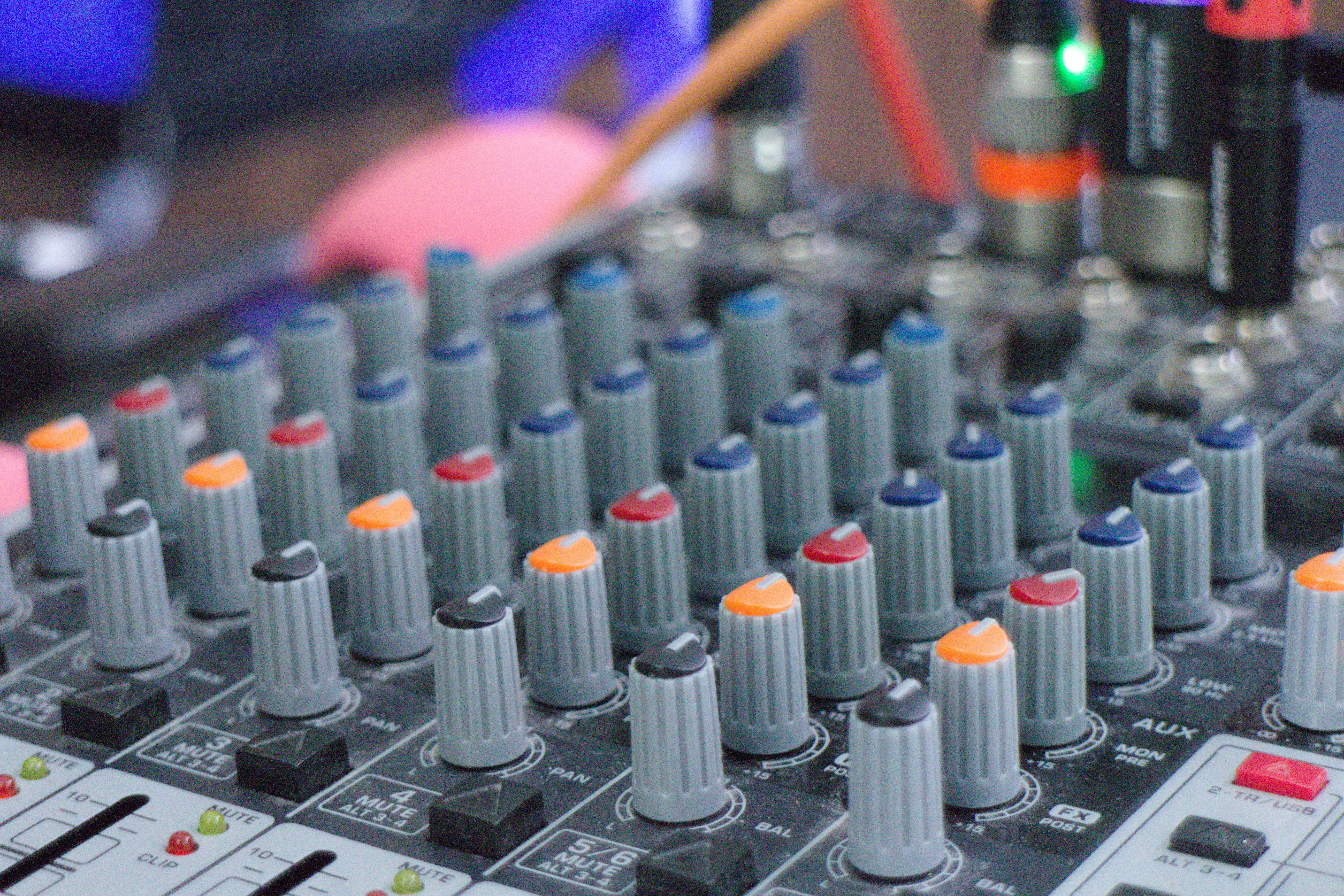Close-up of a multi-channel audio mixer with numerous color-coded knobs and labeled controls, highlighting the tactile interface and range of adjustments.