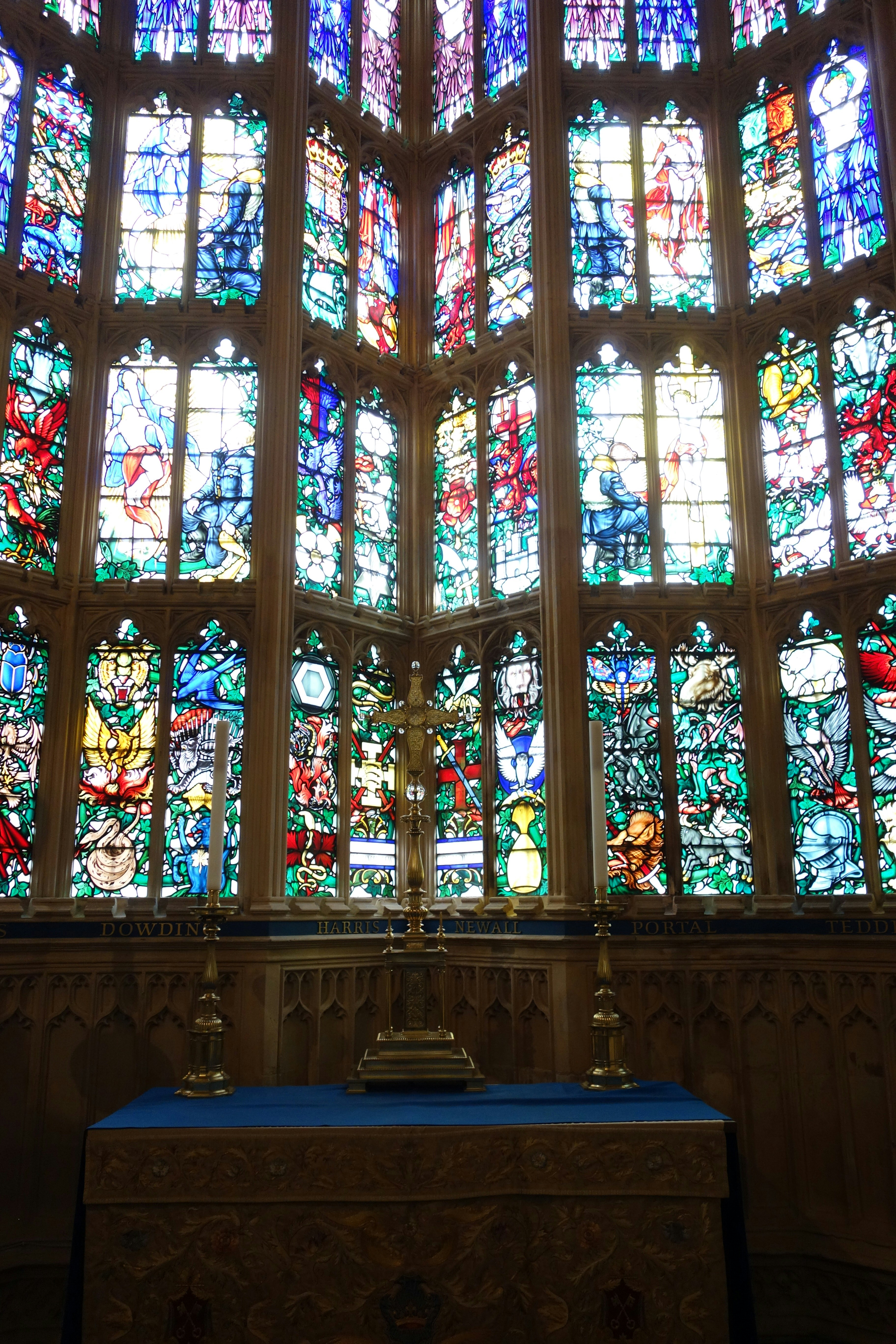 Vibrant church altar set against towering stained glass windows, casting multicolored light across ornate stonework and ceremonial furnishings. A quiet, reverent interior scene focusing on luminous windows behind a carved altar.