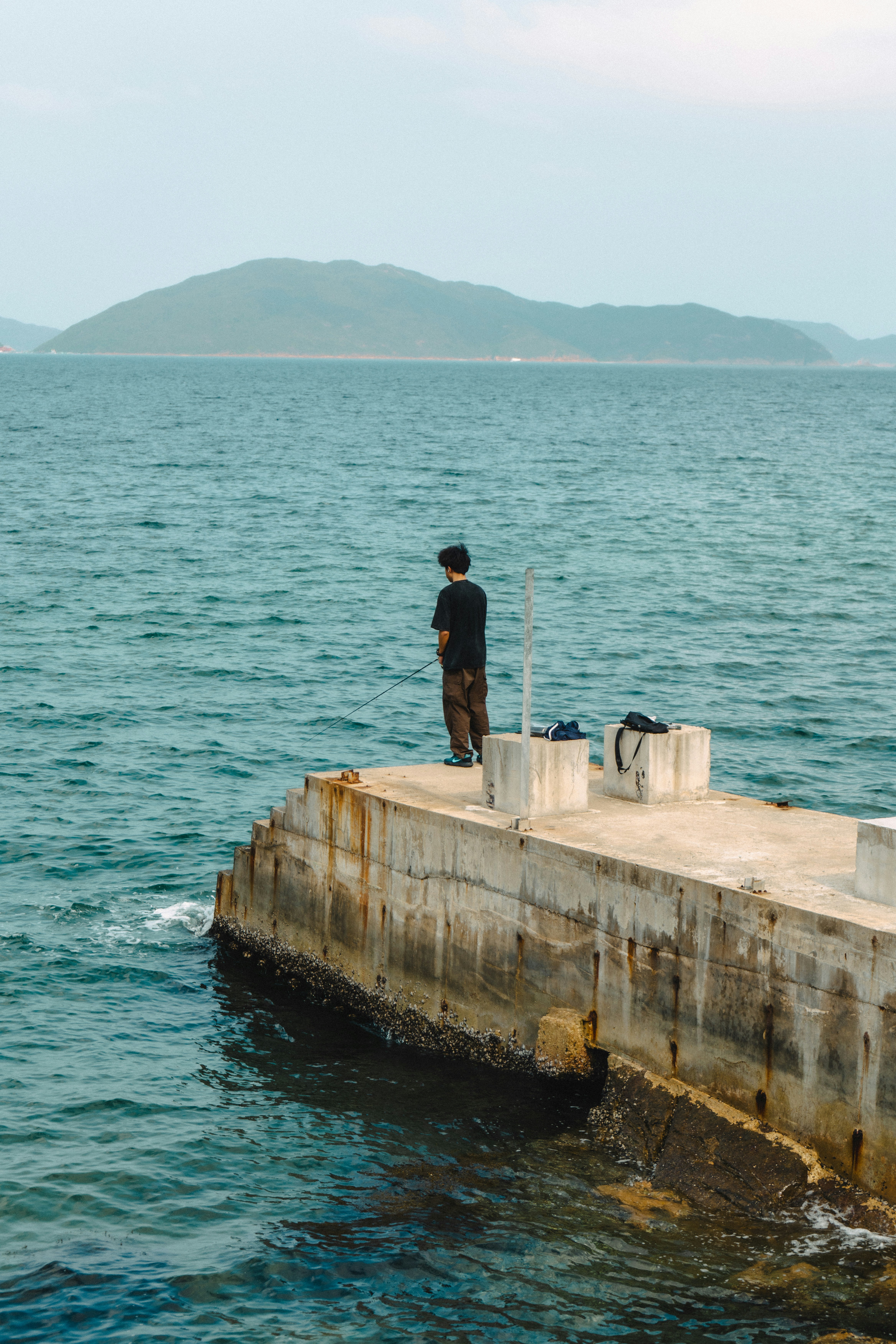  lone angler at the edge of a turquoise sea against distant island hills