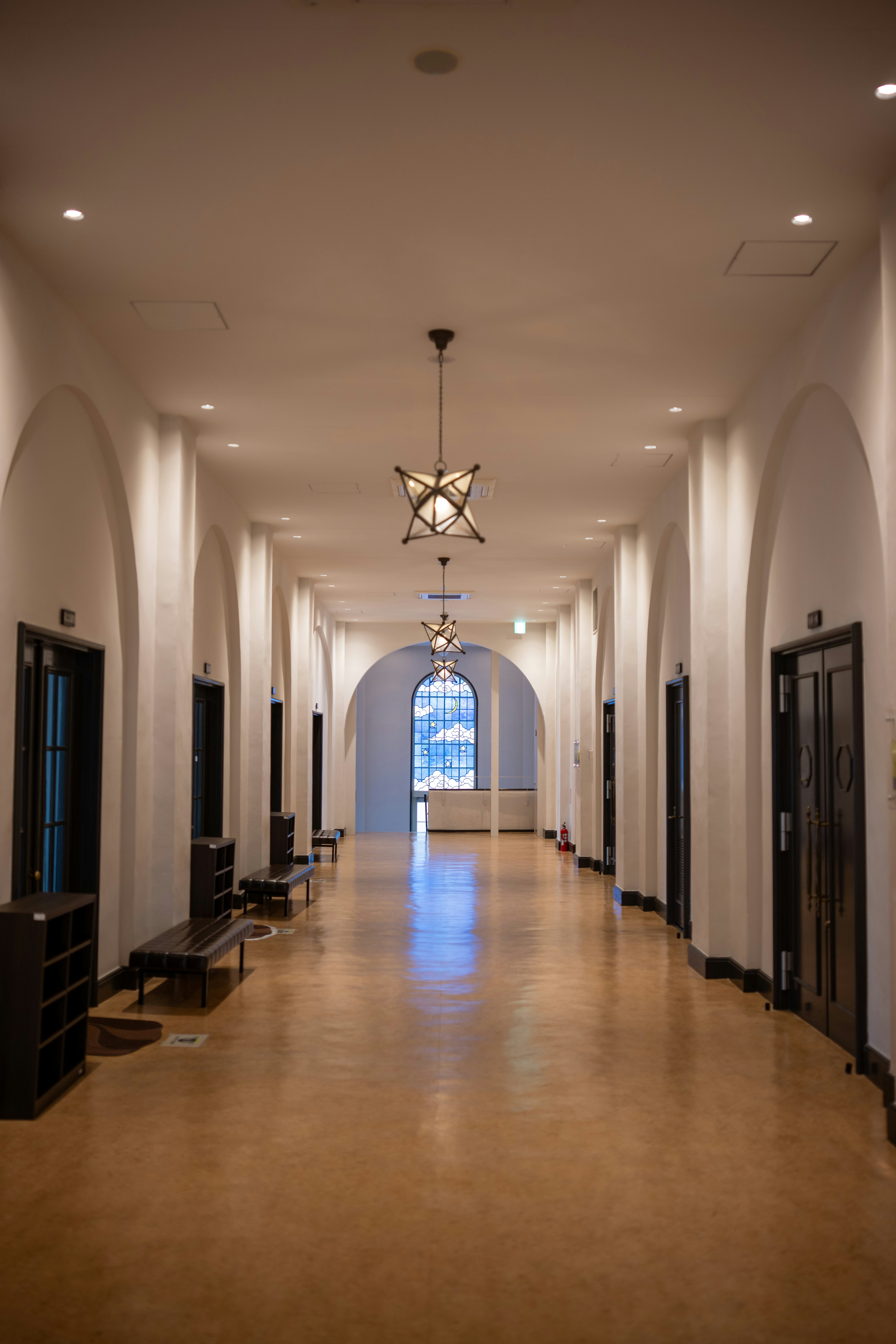 A long hallway with arched white walls, dark doors, and star-shaped pendant lights