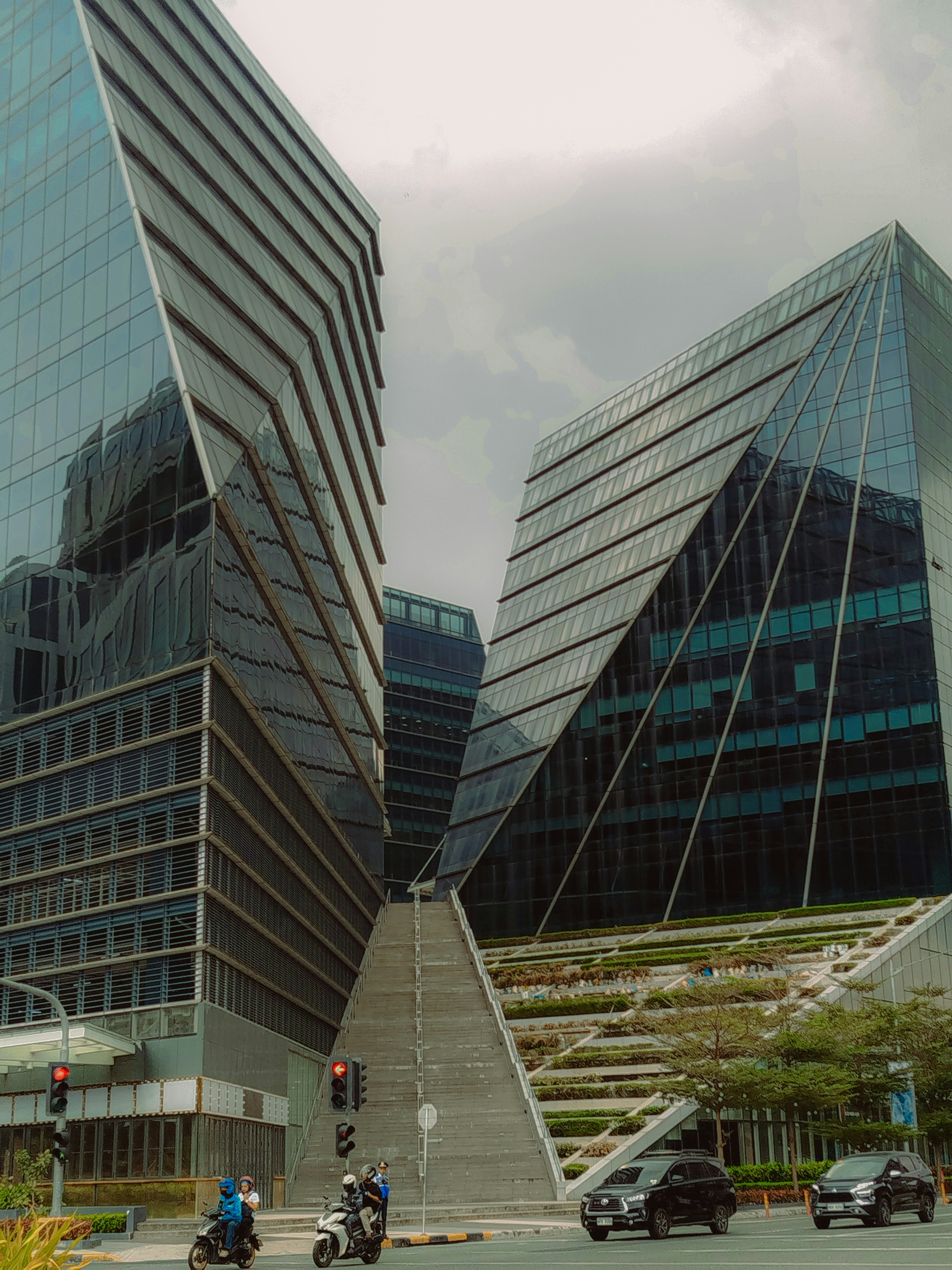 Sleek glass skyscrapers rise on either side, with a central stepped plaza and pedestrians nearby.