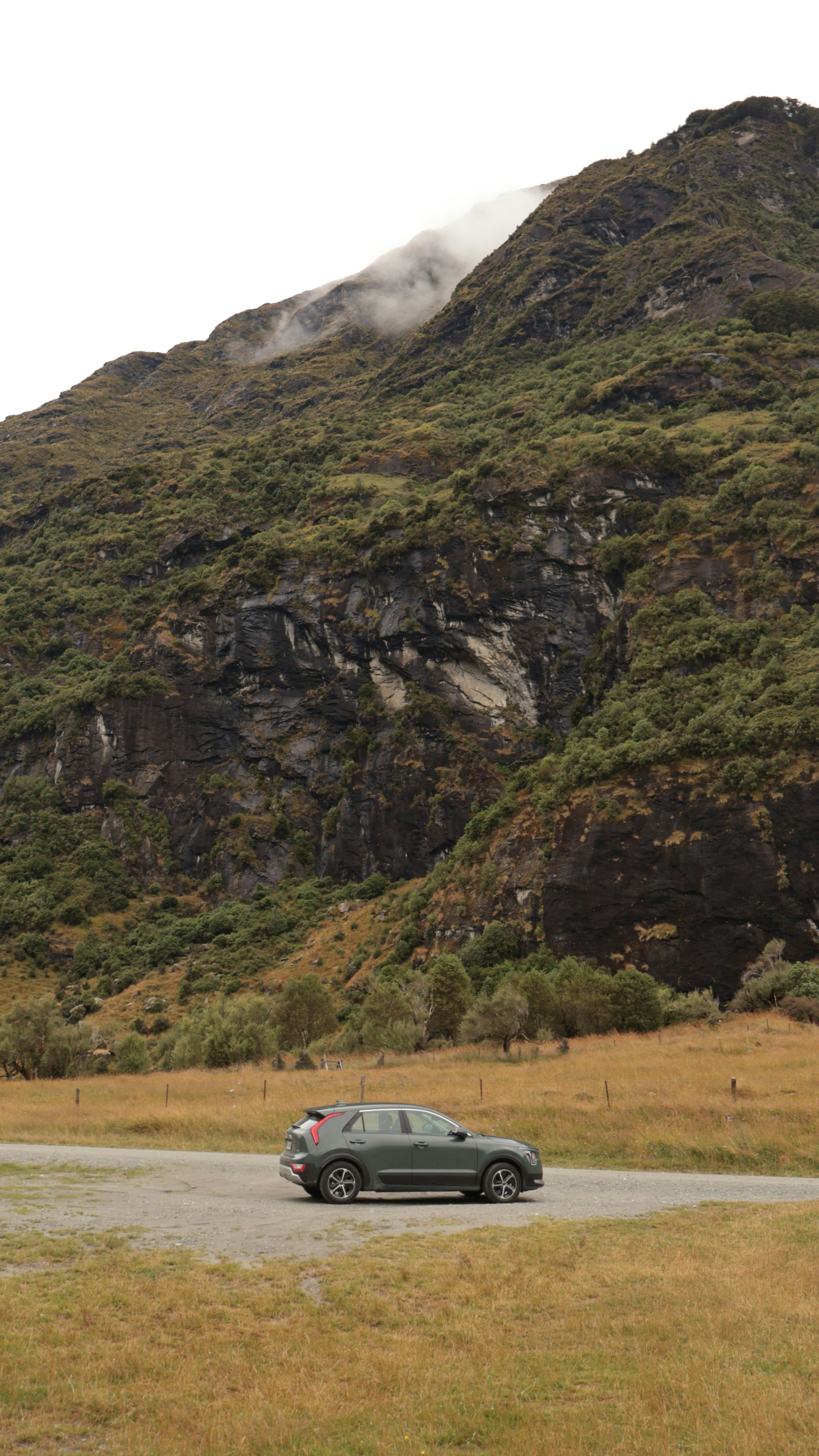 Subtle hillside landscape with a lone car resting on a gravel pad, mountains rising behind and a misty low cloud over the ridge.