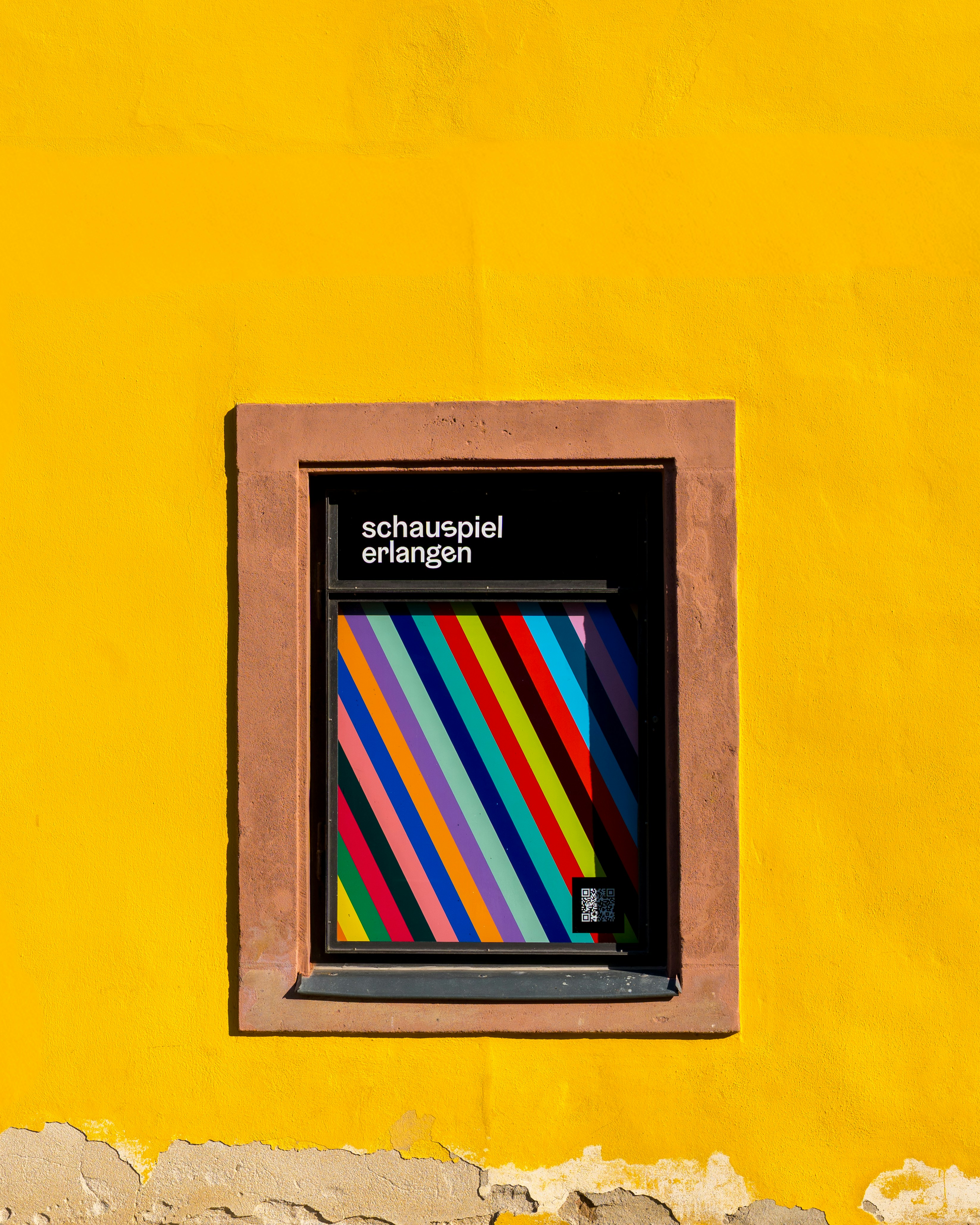 A window with a colorful striped pattern on a bright yellow wall