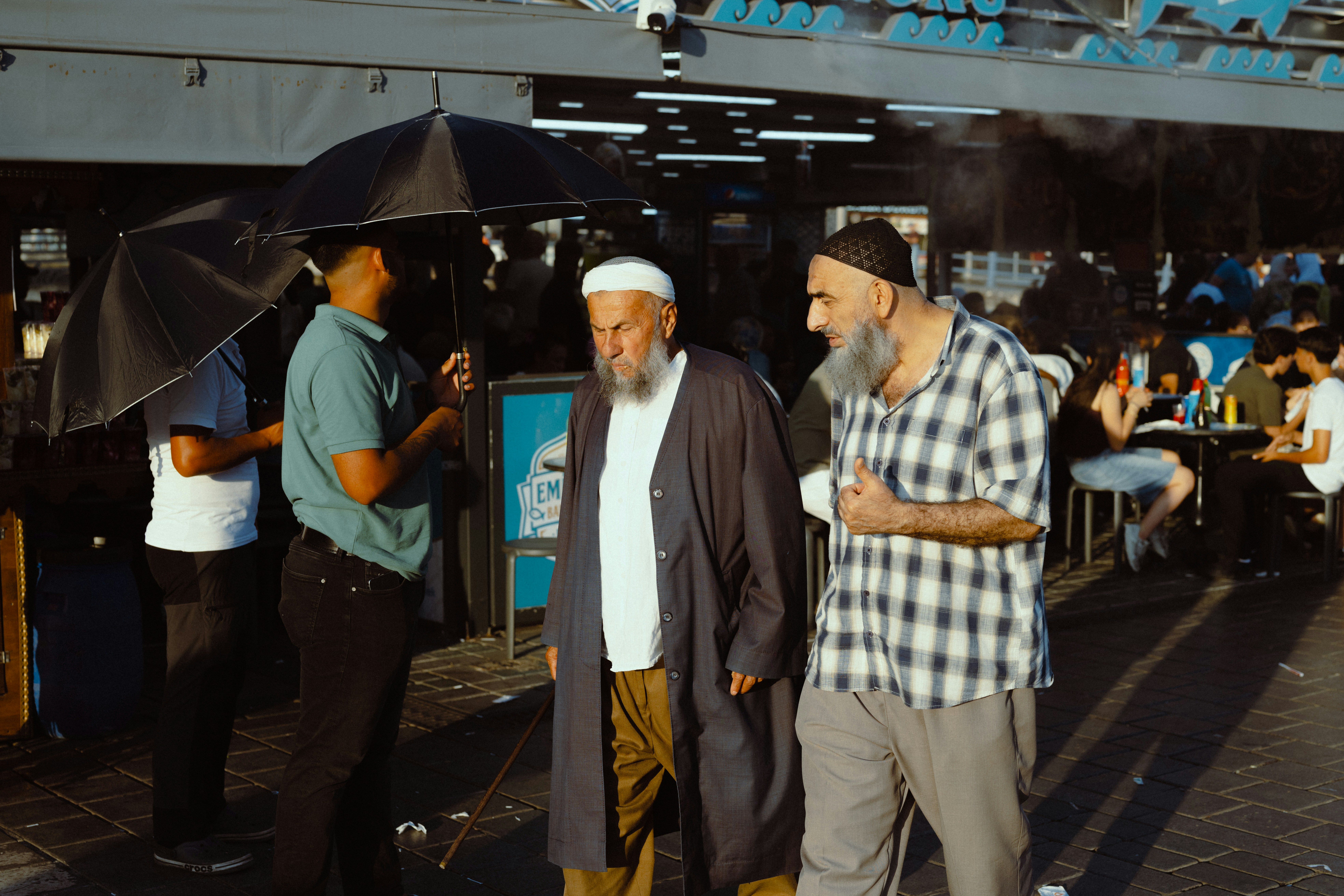 Two elderly men in traditional attire lead a quiet moment under city shadows