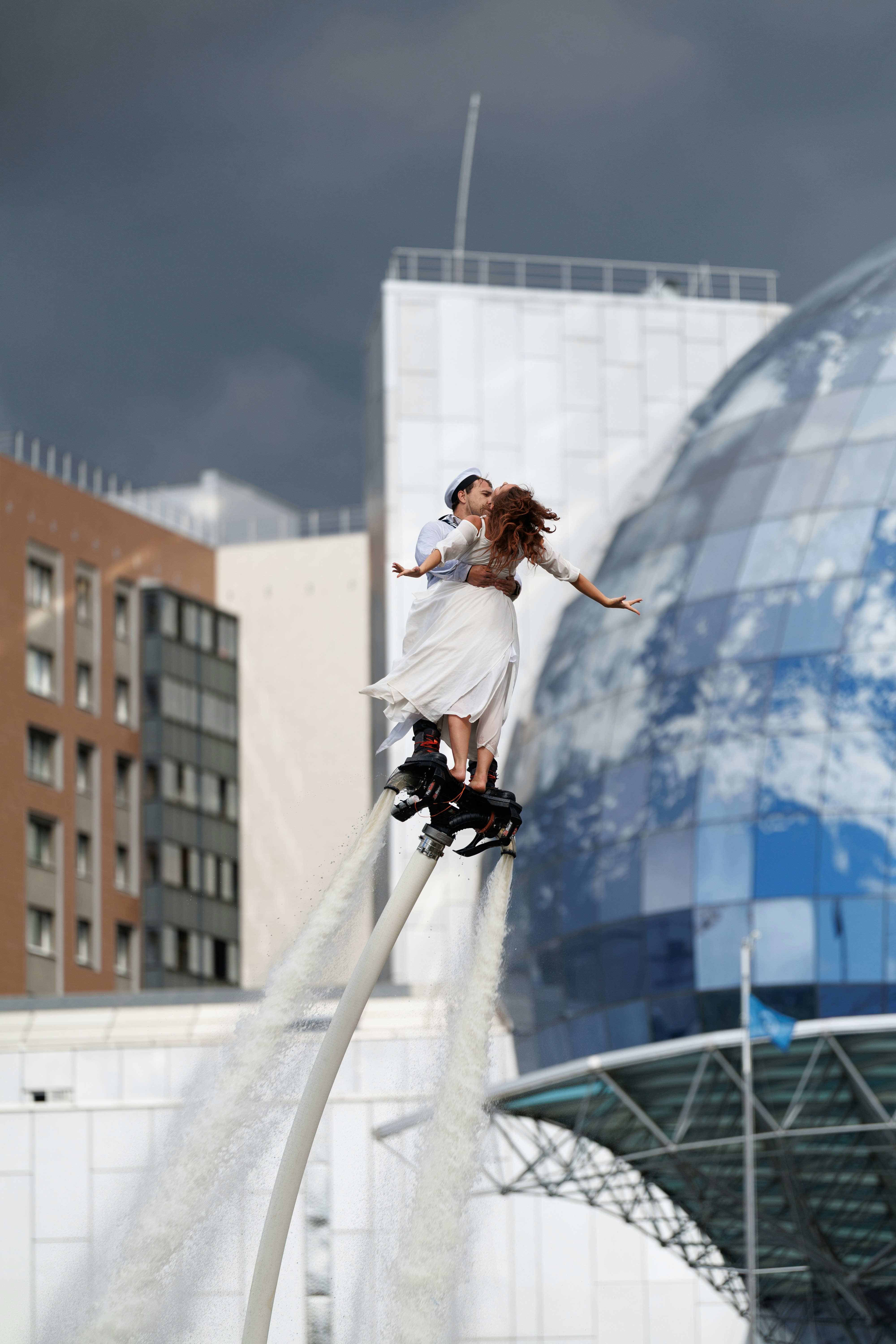 Aerial Embrace: Lovers Ride the Jet of Water Above a Modern City