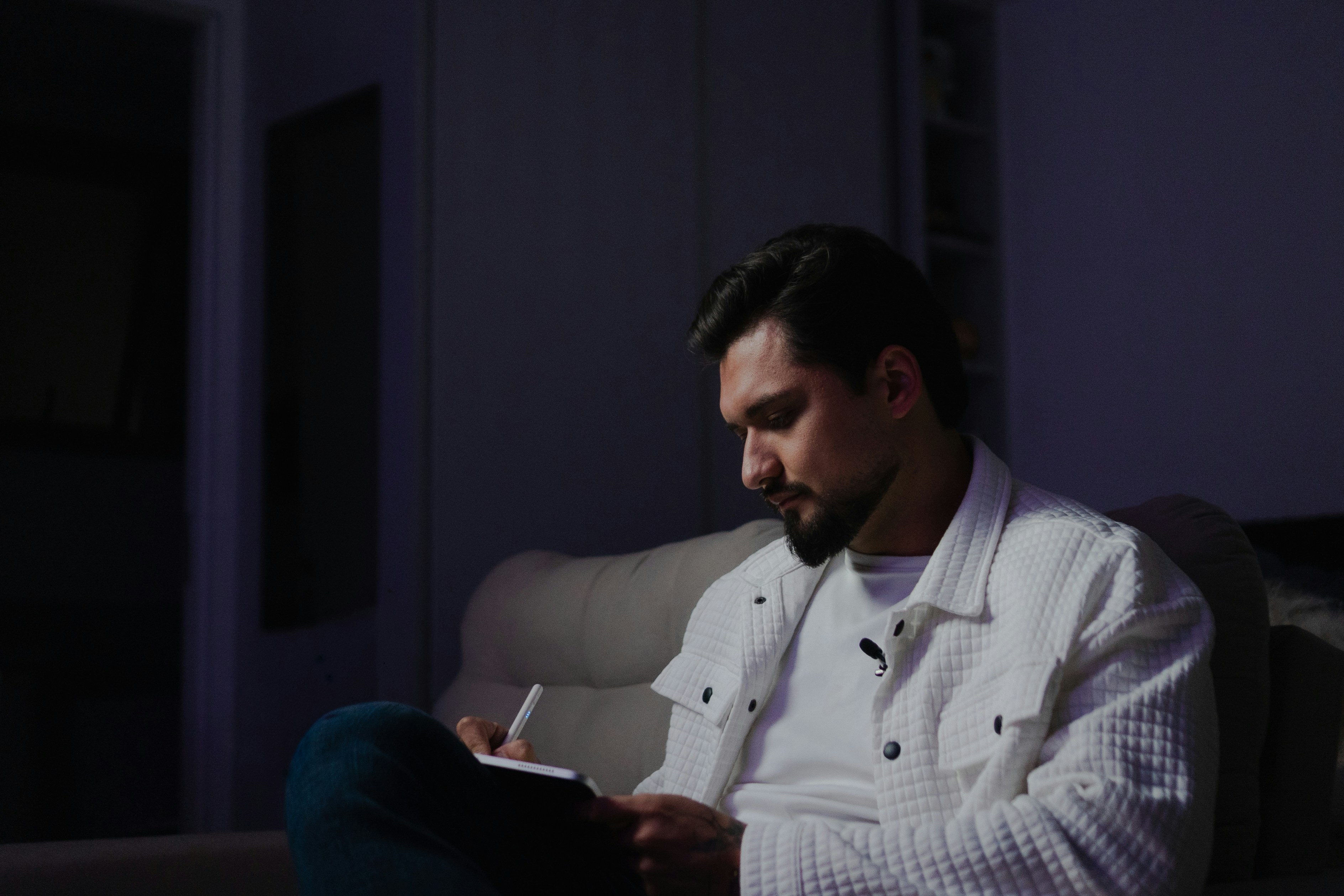 Quiet Creator: A man writes in low light on a cozy couch