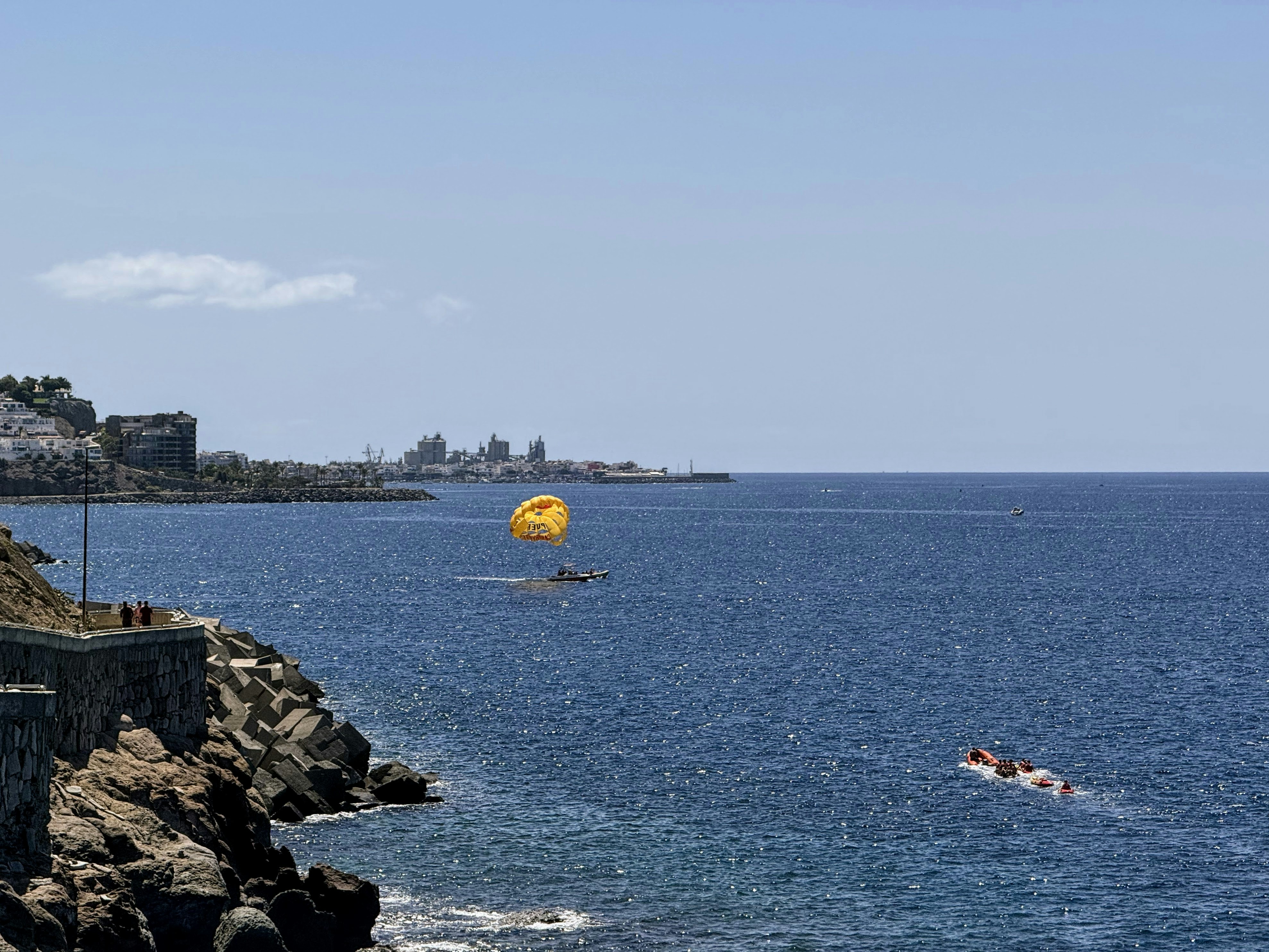 Paragliding dot over a sunlit sea from rocky shoreline