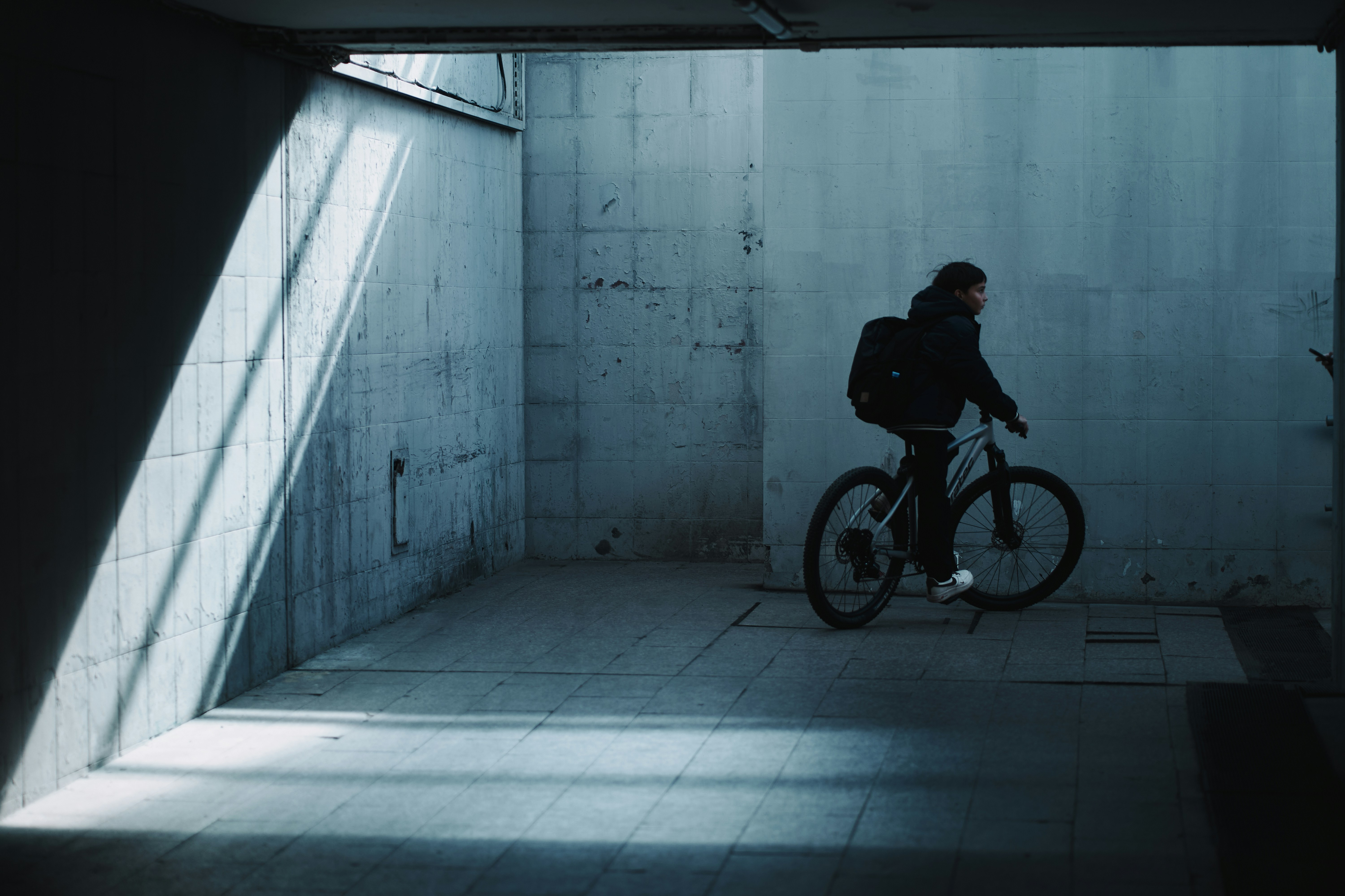  rider in a shadowed underpass: the lone cyclist against cold concrete