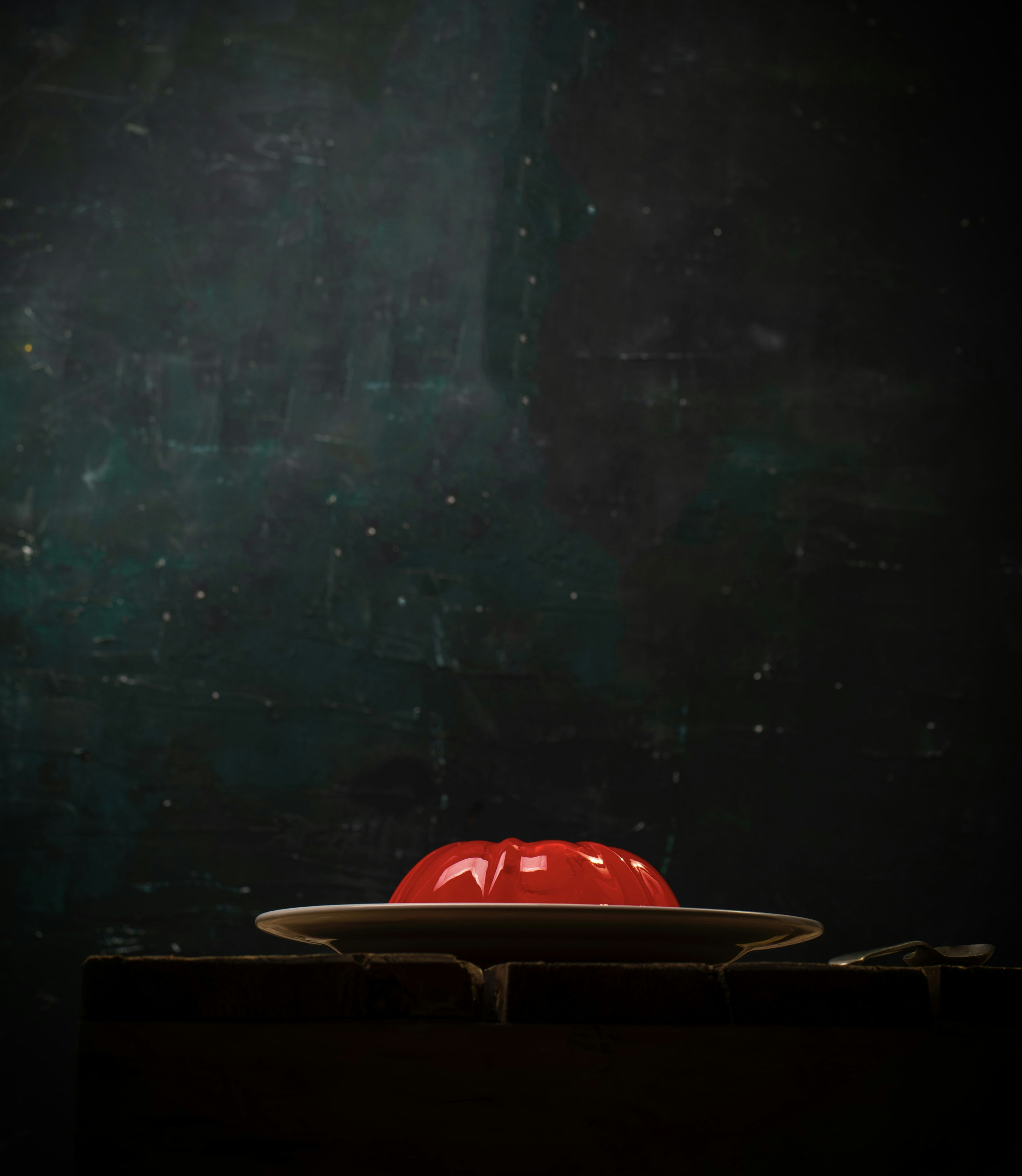 A bright red gelatin mold on a white plate against a dark textured background