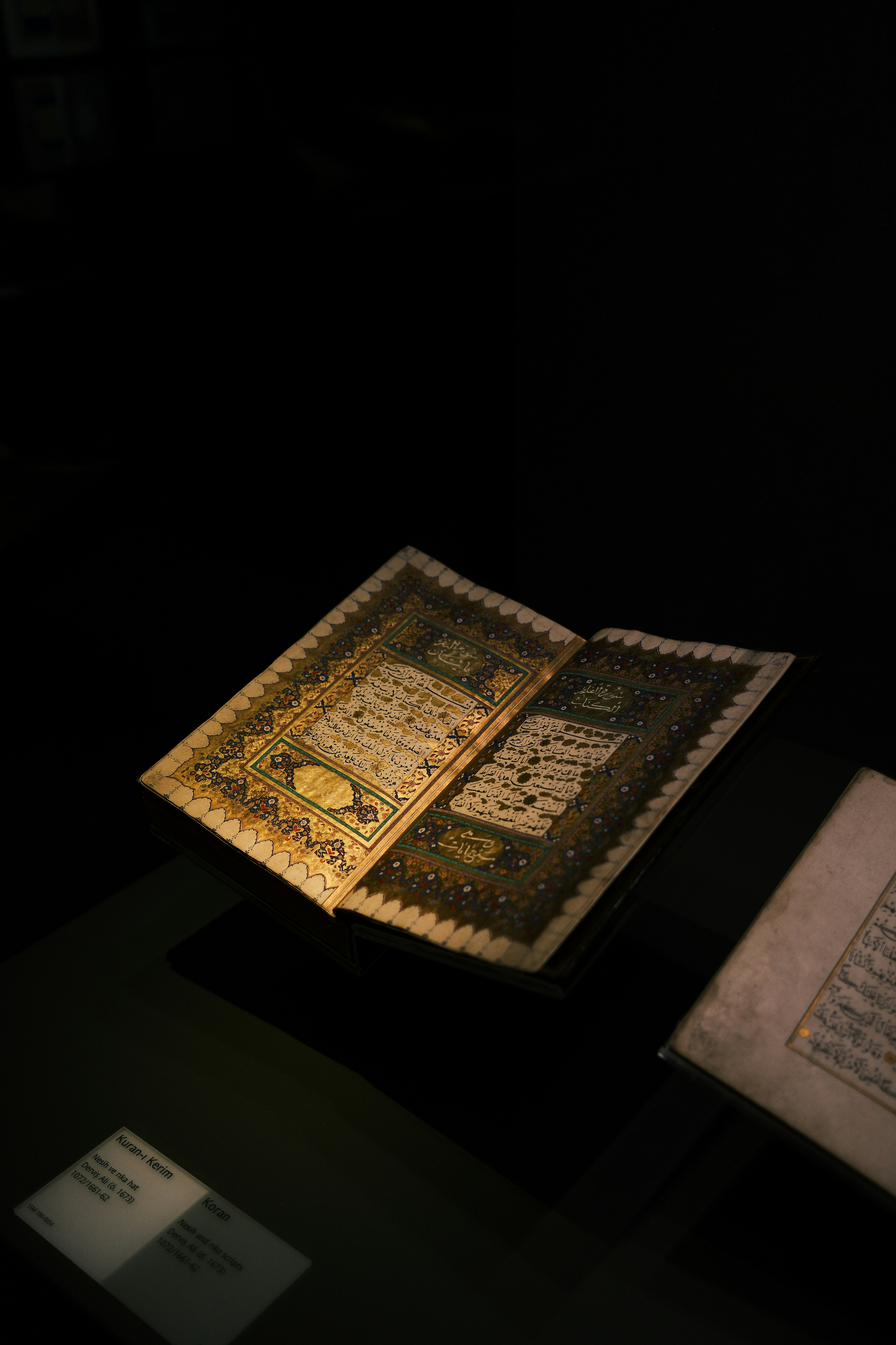  illuminated Quran folio on display: gold-annotated pages in a dim museum case