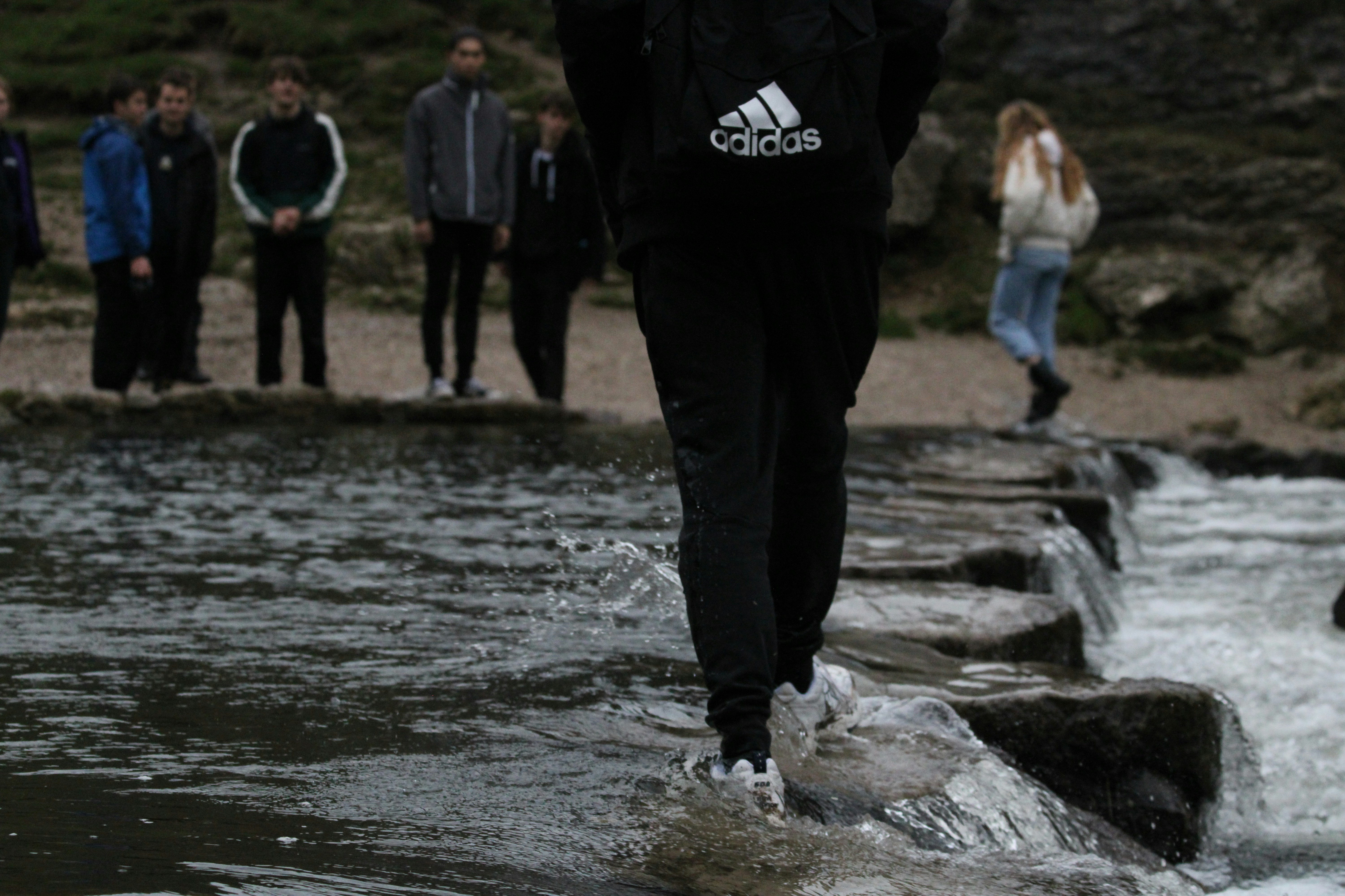 Steps into the tide: sneaker-clad foothold on slick stones amid onlookers