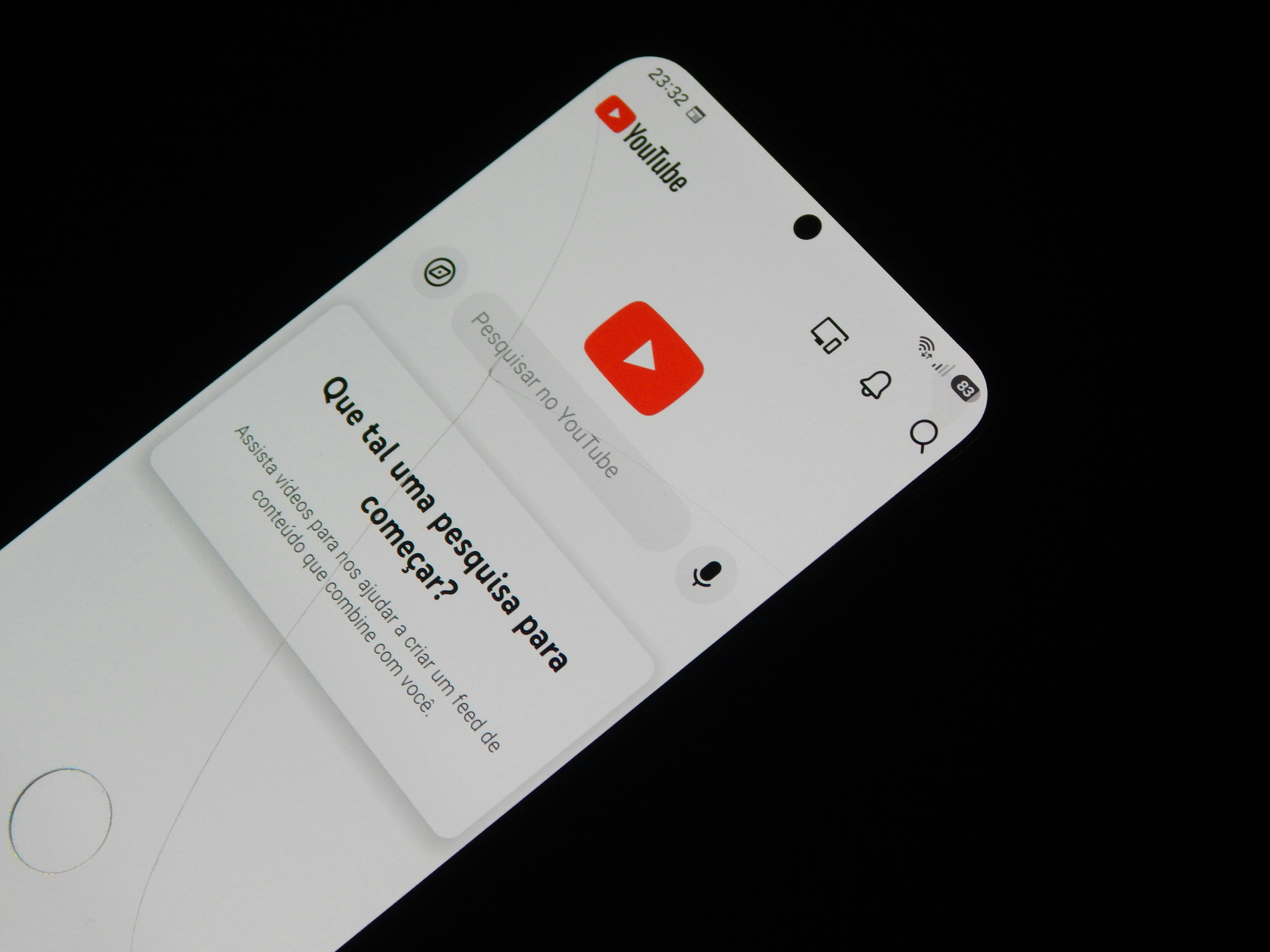 White smartphone screen showing YouTube app with red play icon; device angled against dark background, suggesting a product or screen capture. The image emphasizes a clean device display in a low-light setup.