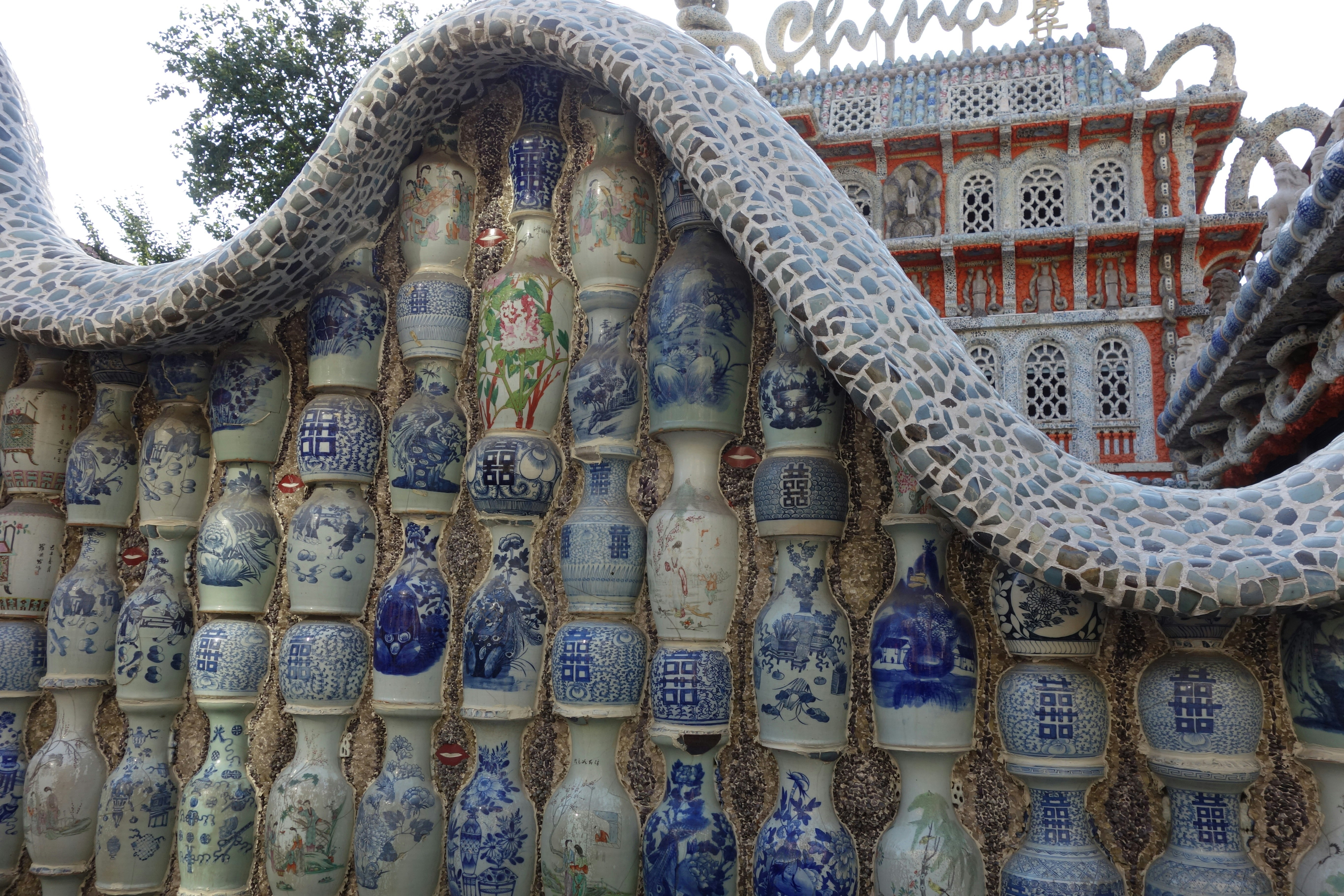 A wall covered in stacked ceramic vases with blue-and-white patterns and a serpentine mosaic frame, forming a dense, decorative facade. This is a ceramic installation/architectural detail.