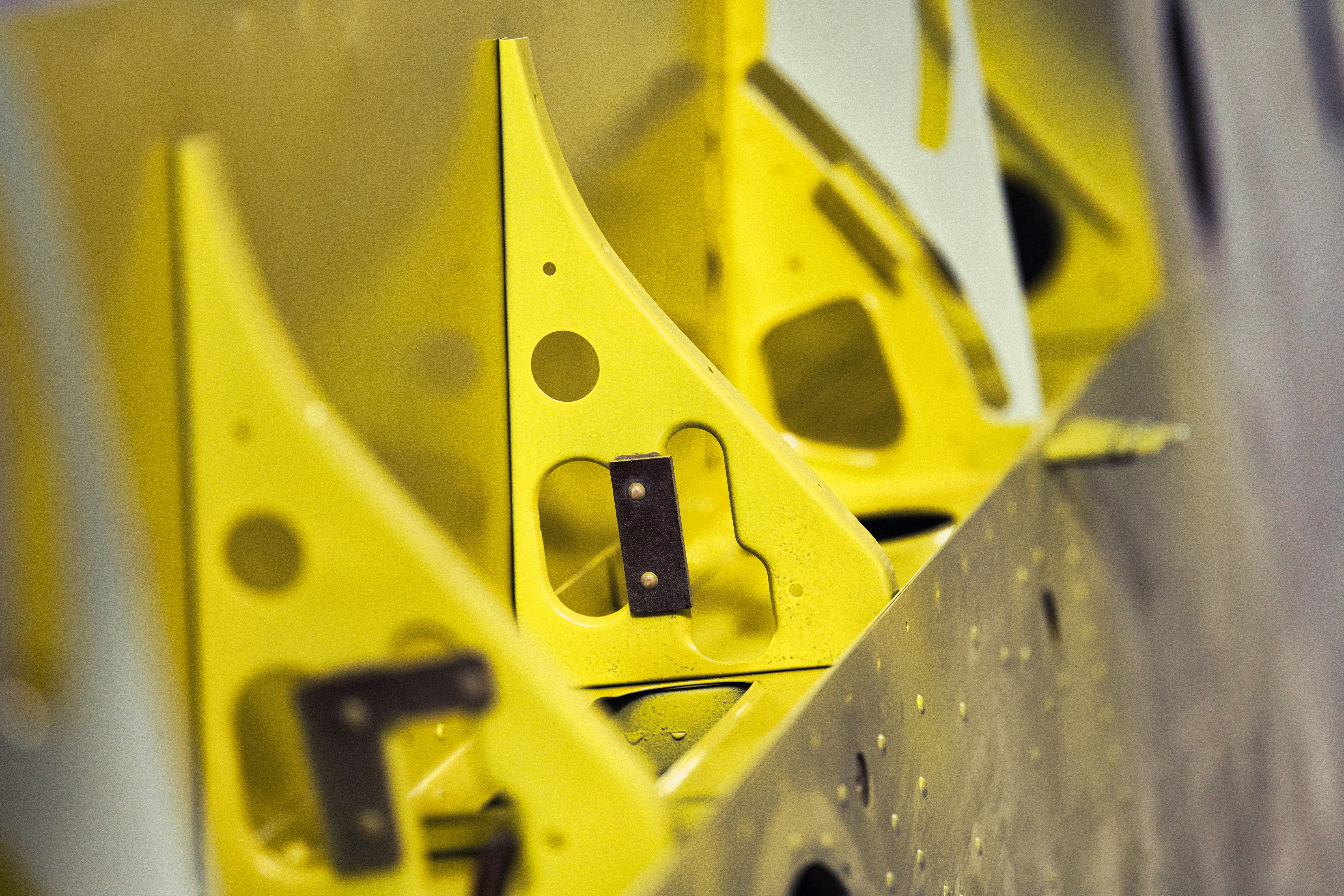 Industrial yellow metal brackets and panels with bolt holes, captured in sharp focus to emphasize repetitive geometry and texture.