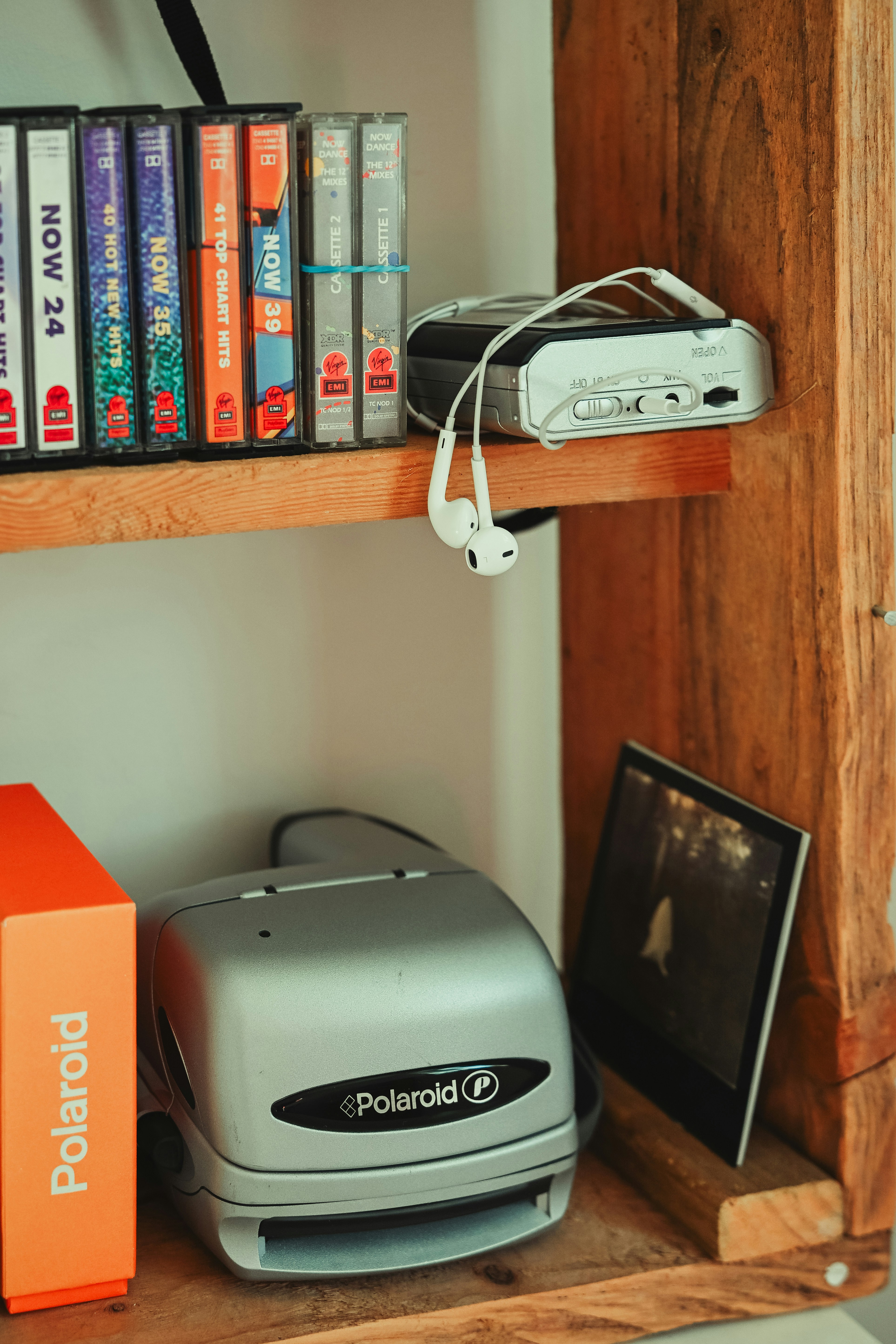 Shelf of Memories: A Polaroid and Earbuds Rest Under Wooden Shelves