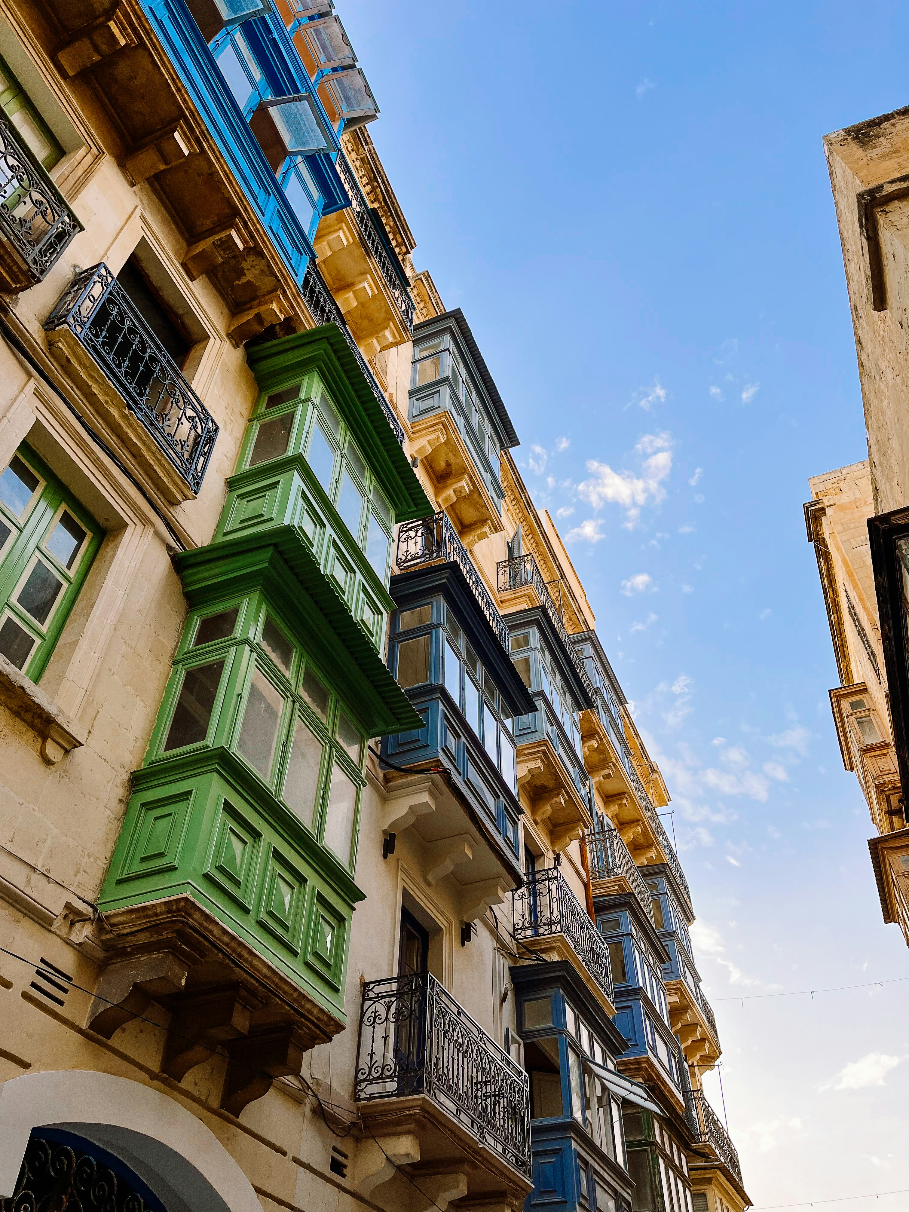 Multi-colored historic balconies line a sunlit street, balconies protruding from stone buildings with a clear blue sky above.